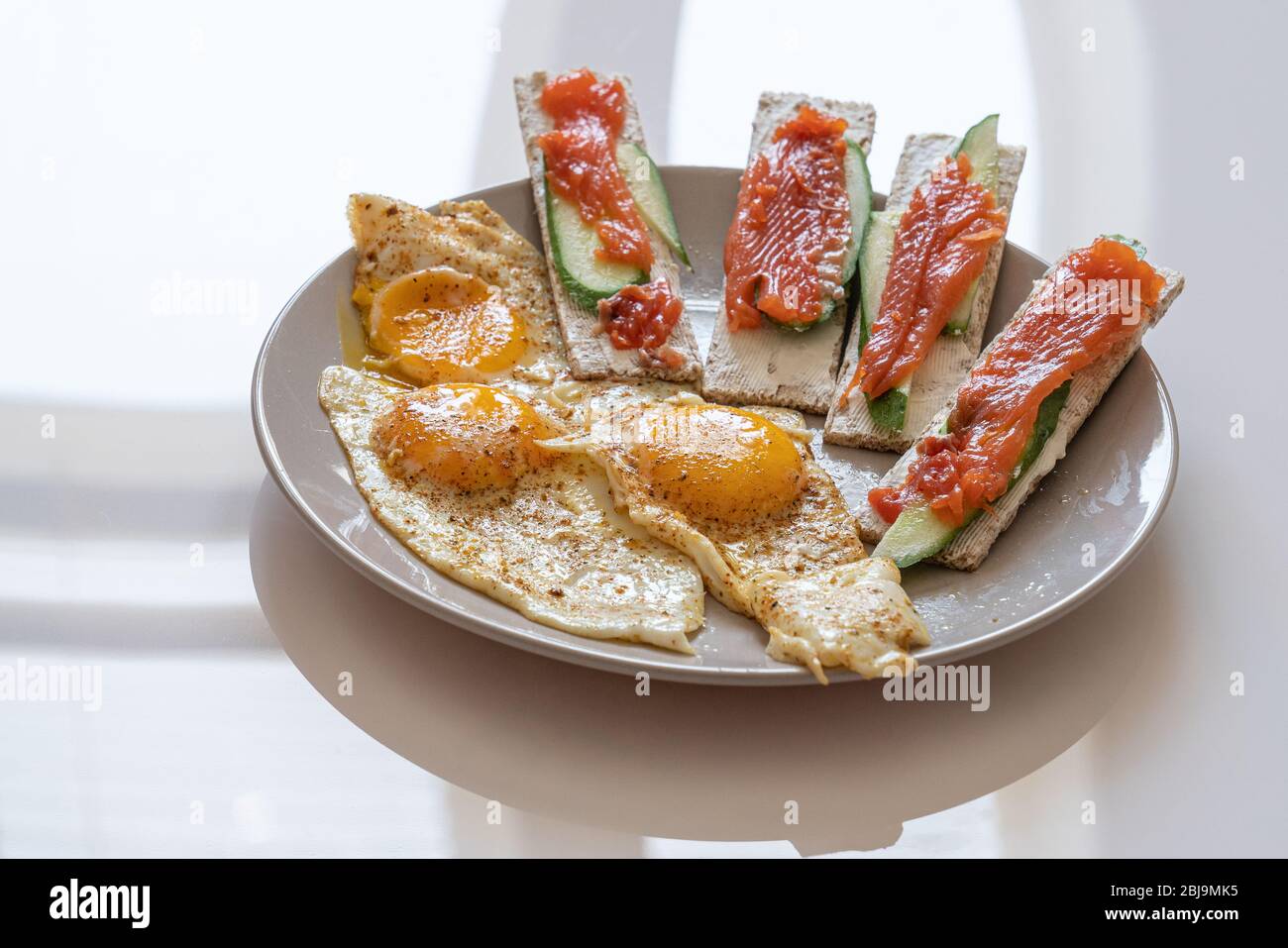 Three toasts with red fish, cucumber and three eggs on white plate over ...