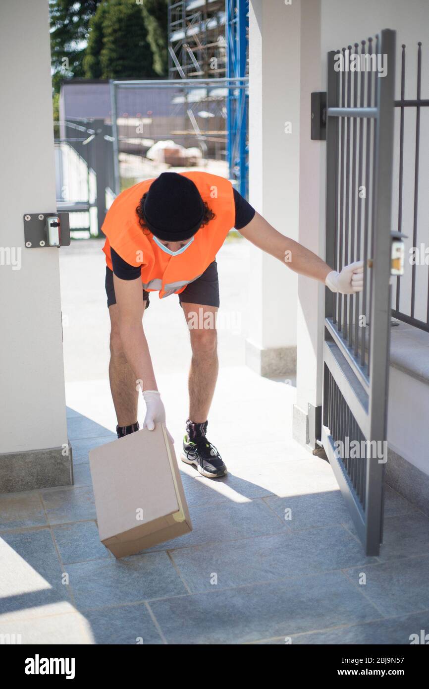 Young delivery man leaving parcel box on the floor at gate wearing ppe ...