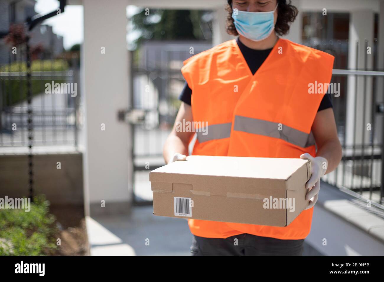 Young delivery man with parcel box in outdoor context with ppe, gloves ...