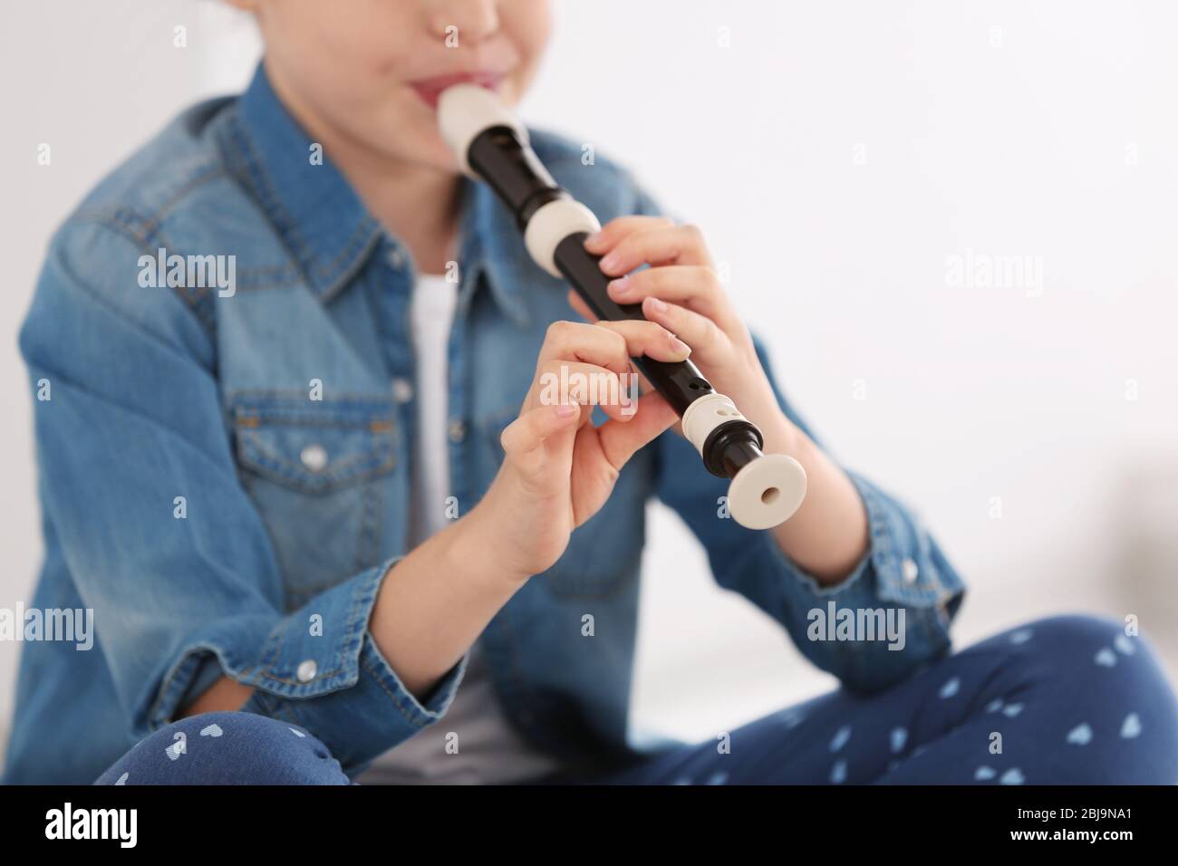 Little girl playing flute on light background Stock Photo - Alamy