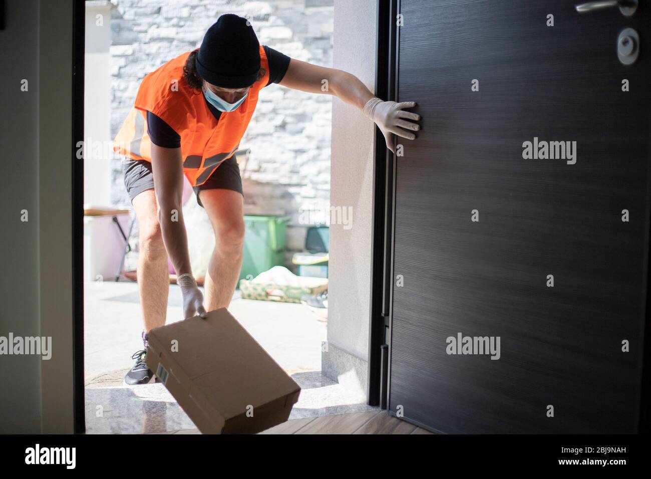 Young delivery man leaving parcel box but touching front door, wearing ...