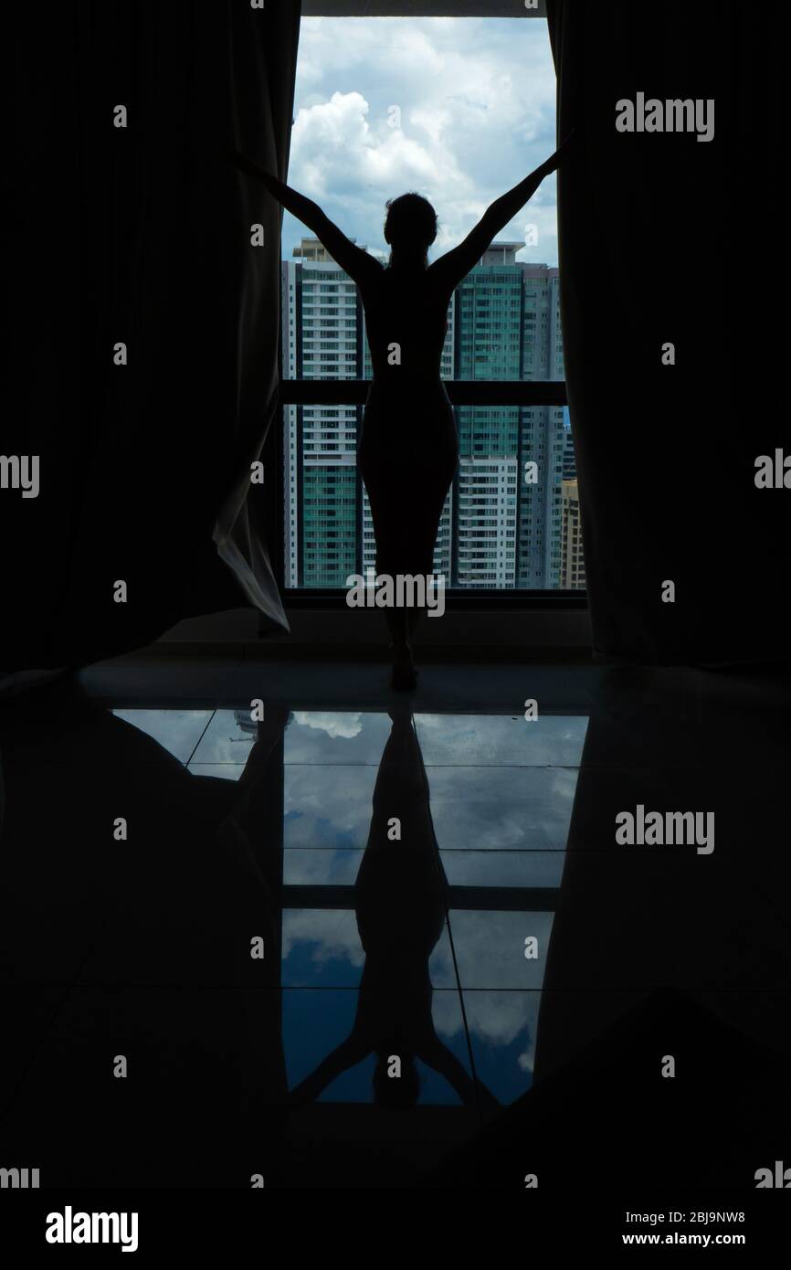 A slender girl is looking at the city through a large window. High ...