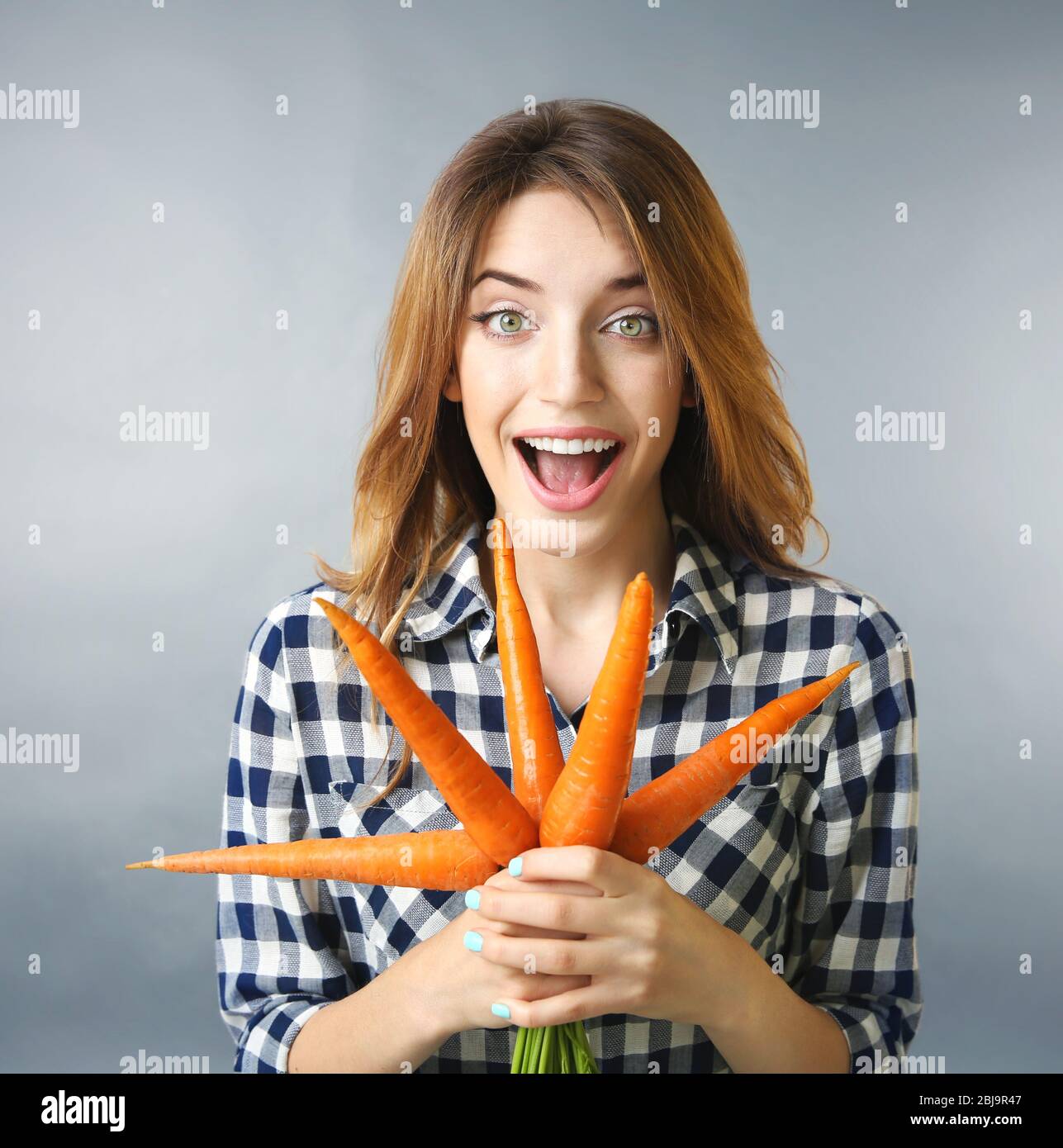 Beautiful girl eating carrot on grey background Stock Photo - Alamy