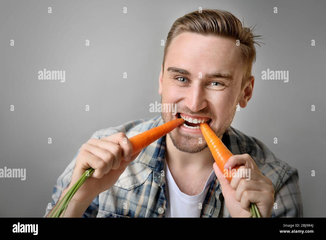 Handsome man eating carrot on grey background Stock Photo - Alamy