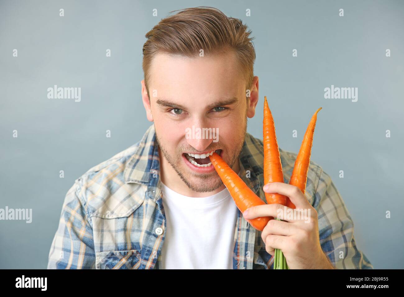 Handsome man eating carrot on grey background Stock Photo - Alamy
