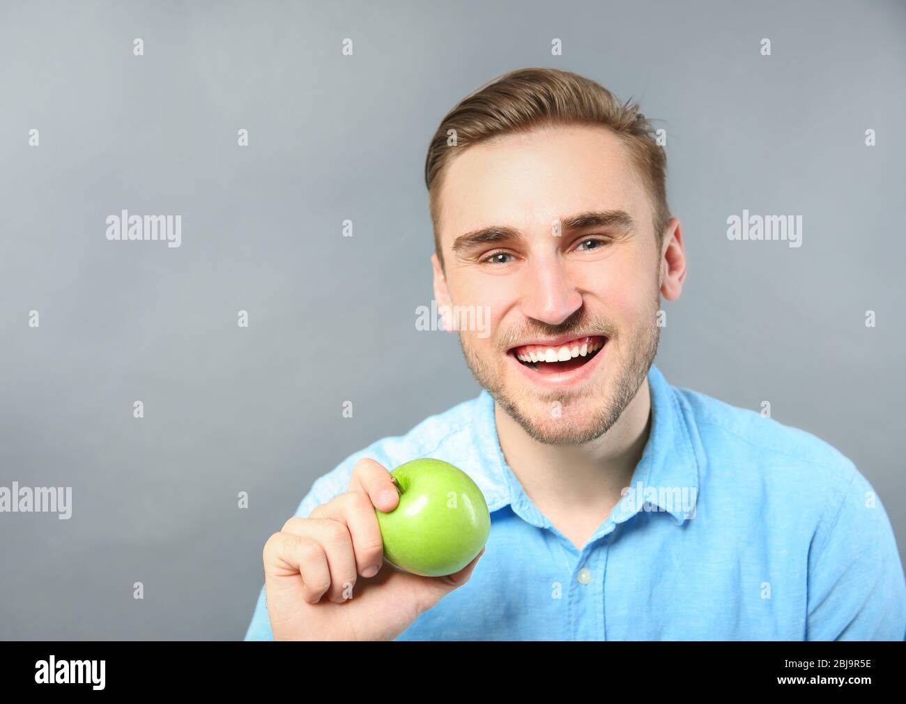 Handsome man eating apple on grey background Stock Photo - Alamy