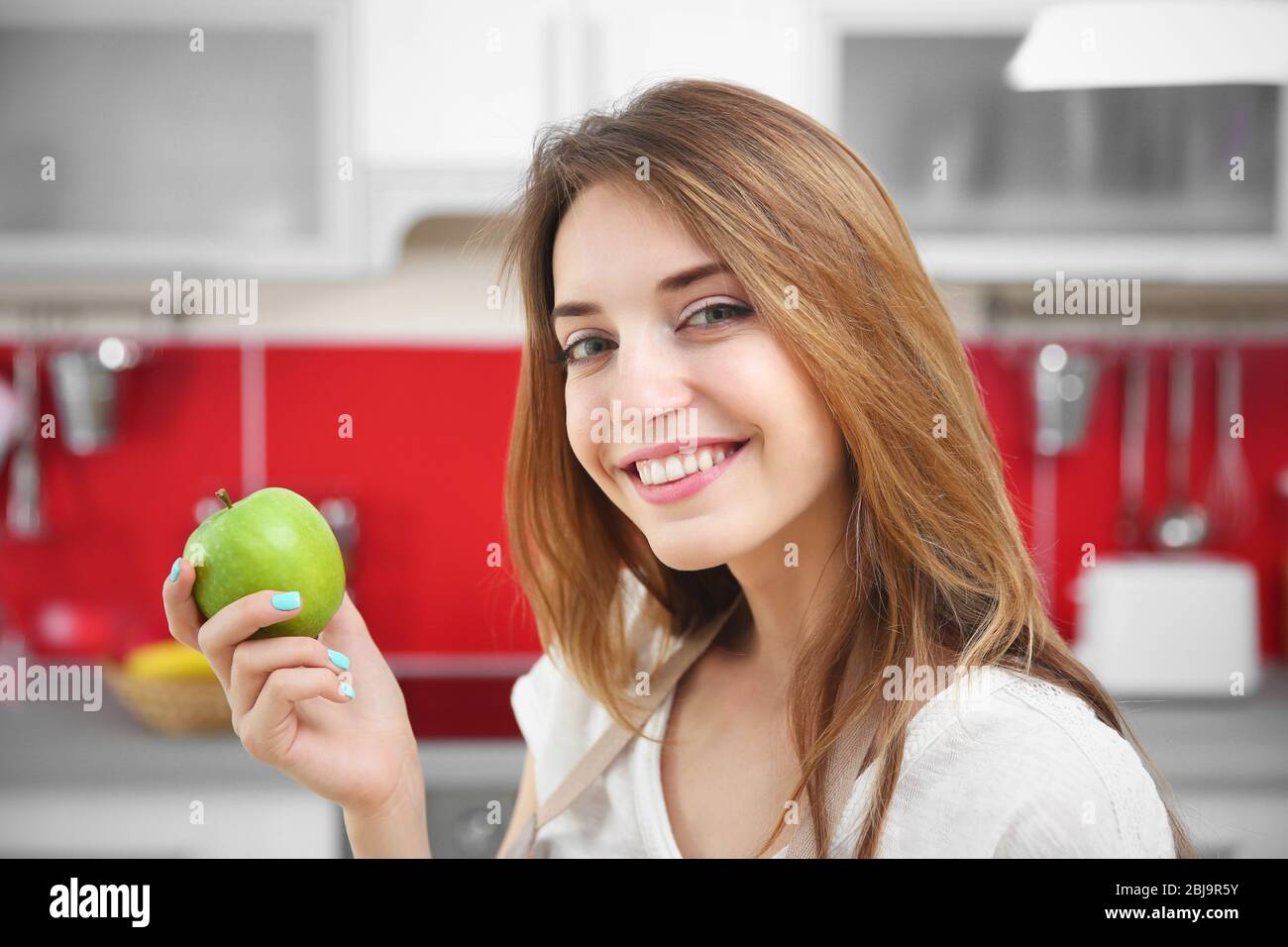 Beautiful girl eating apple in kitchen Stock Photo - Alamy