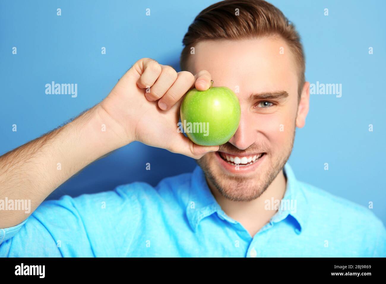 Handsome man eating apple on blue background Stock Photo - Alamy