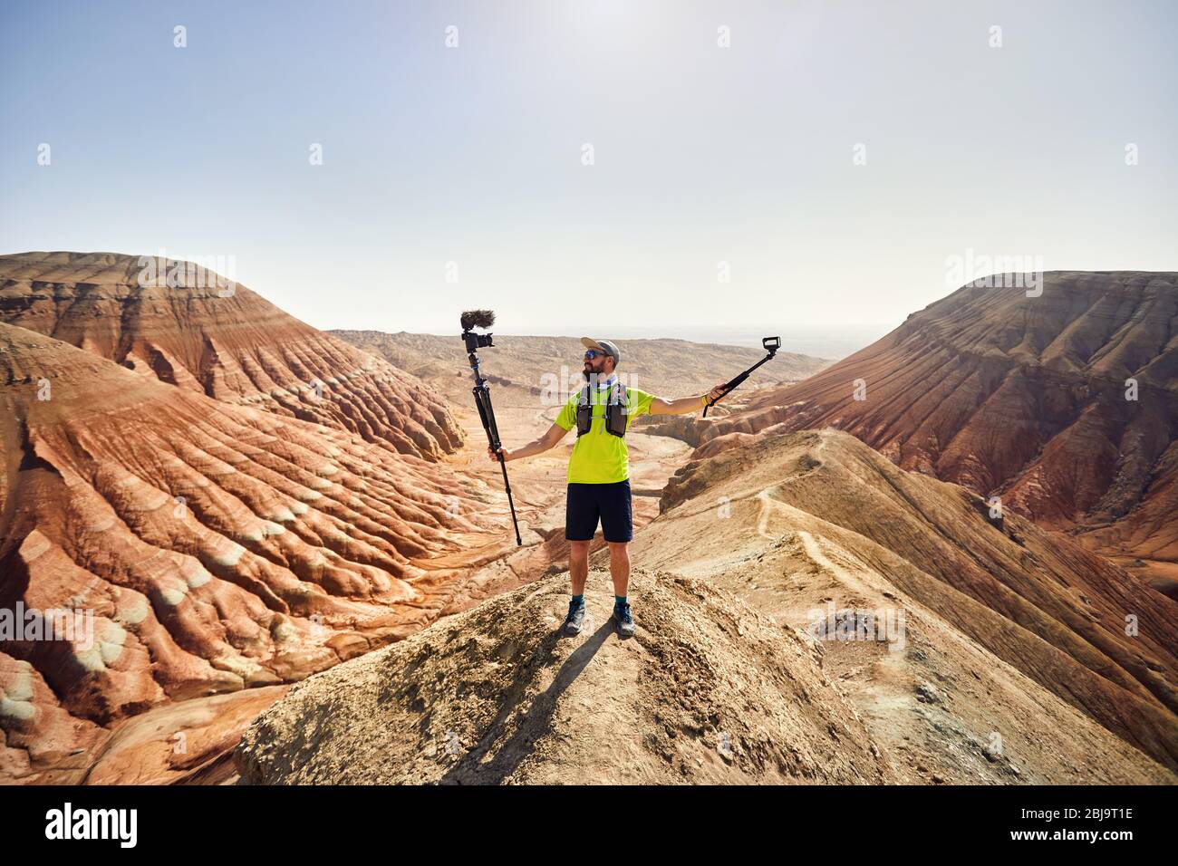 Bearded man holding two cameras on the top of the mountain in the ...