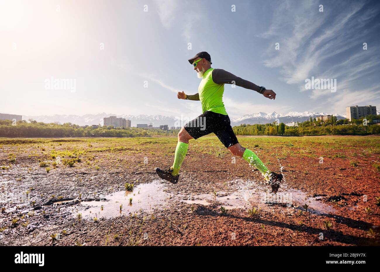 Man with grey beard running on the dirty trail at mountain background ...