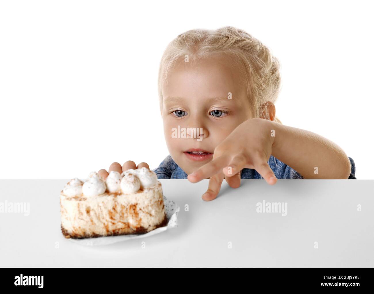 Funny little girl hiding behind white table and looking at tasty cake ...