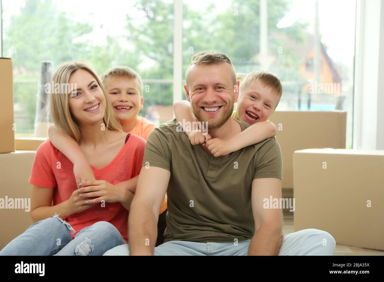 Happy family with cardboard boxes sitting on wooden floor Stock Photo ...