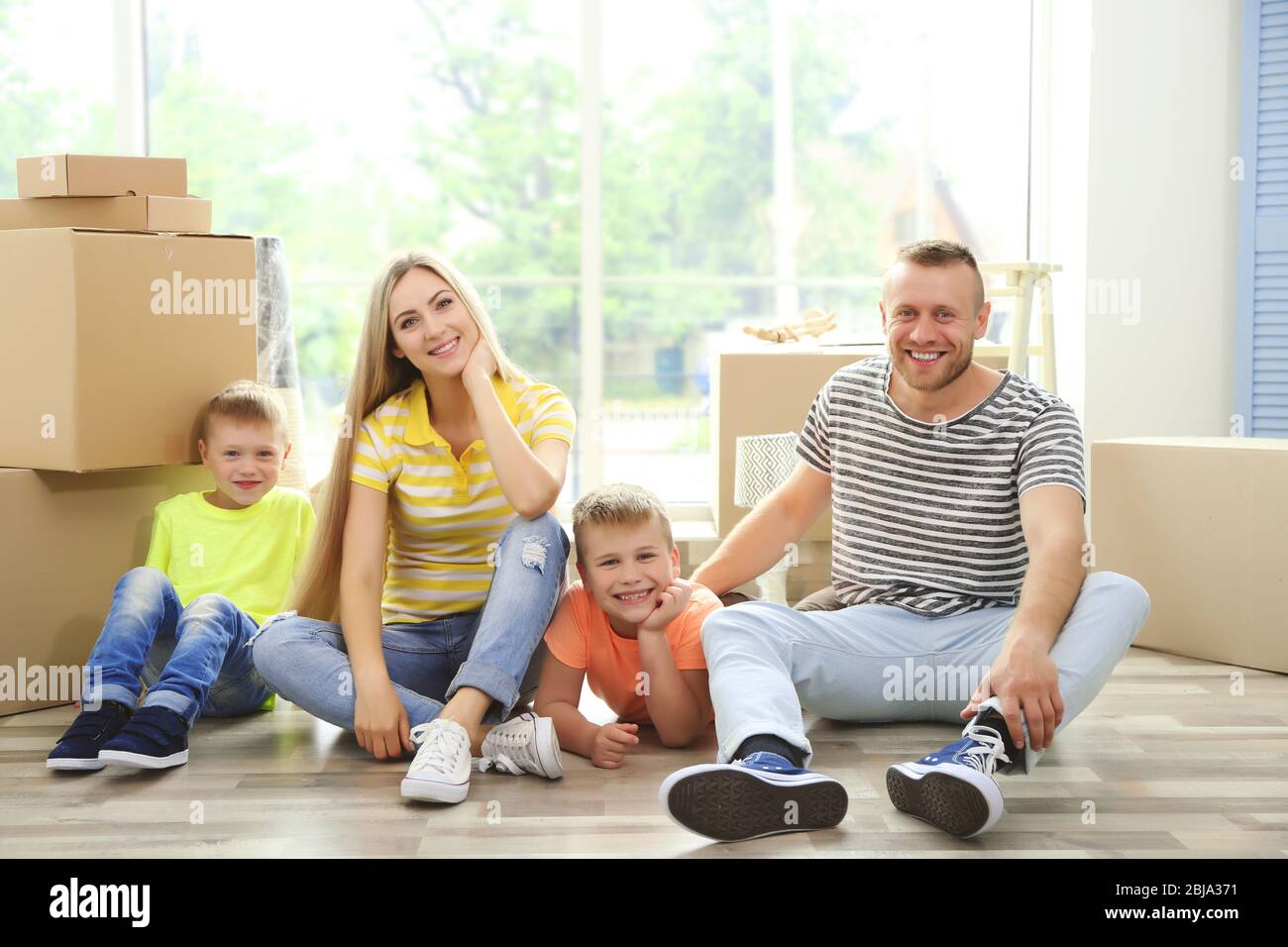 Happy family with cardboard boxes sitting on wooden floor Stock Photo ...