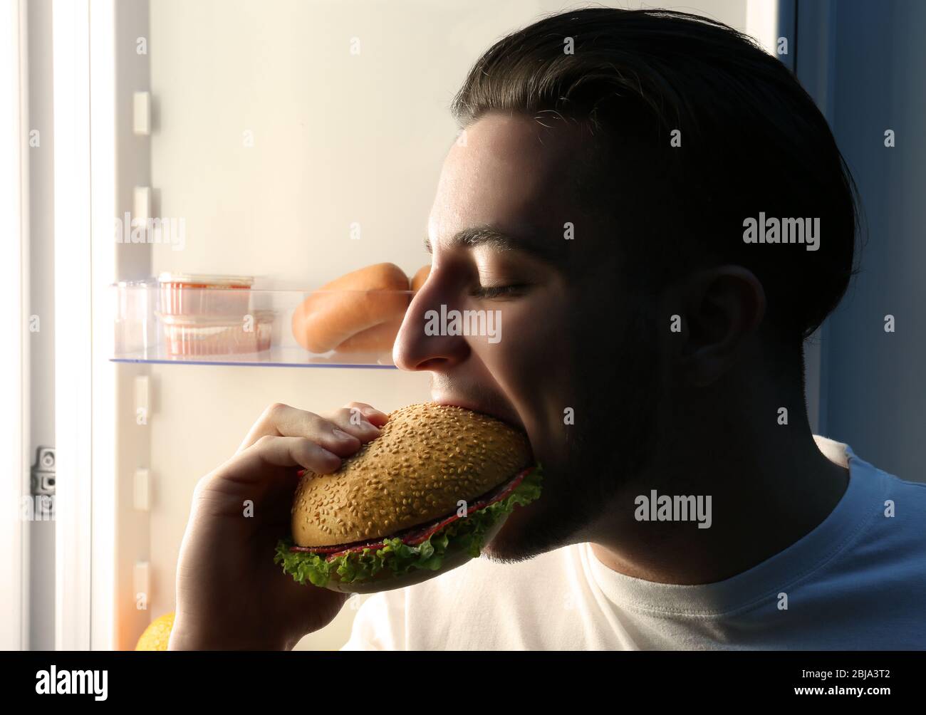Handsome man eating sandwich in kitchen. Unhealthy food concept Stock ...