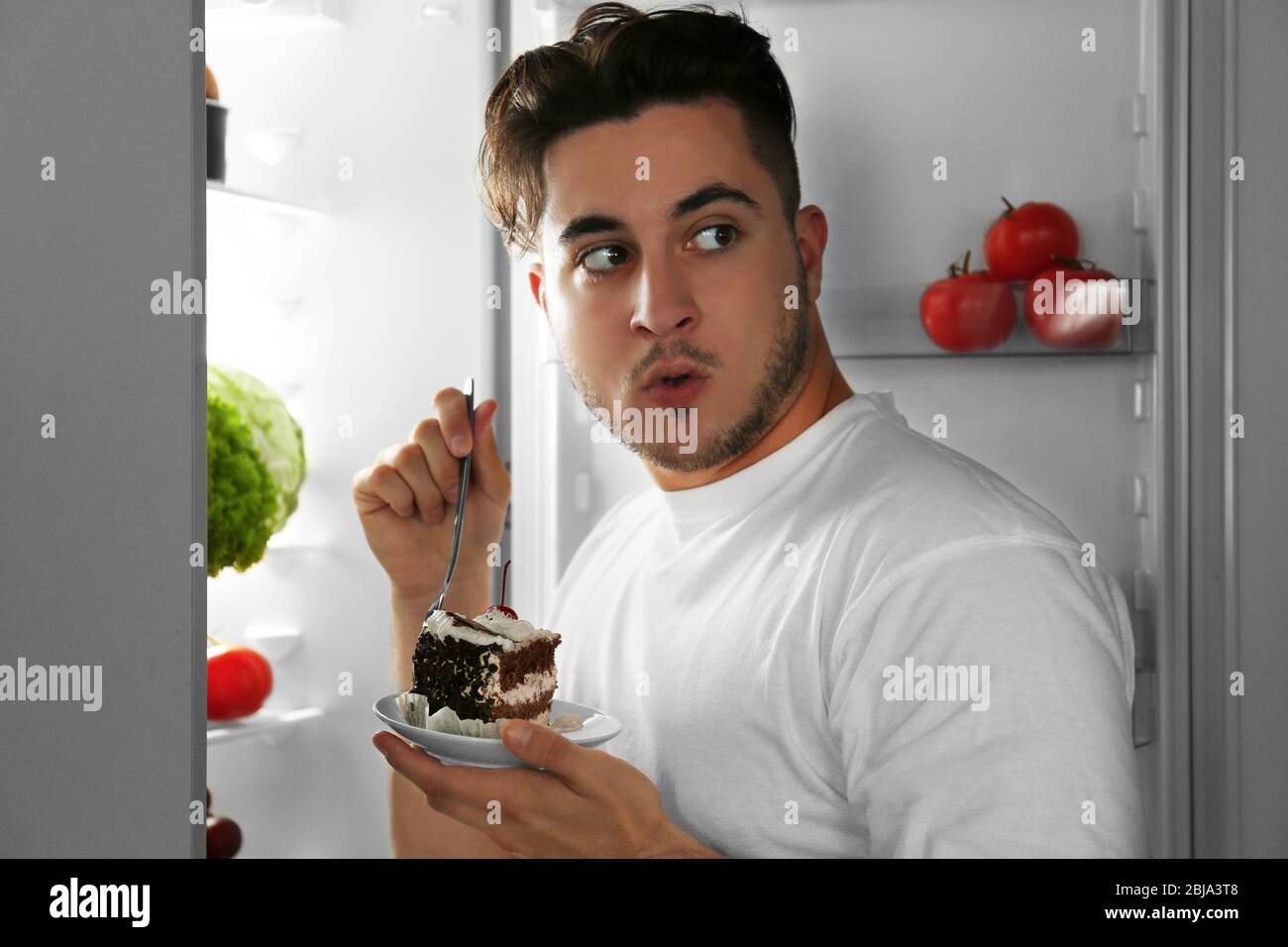 Handsome man eating cake in kitchen. Unhealthy food concept Stock Photo ...