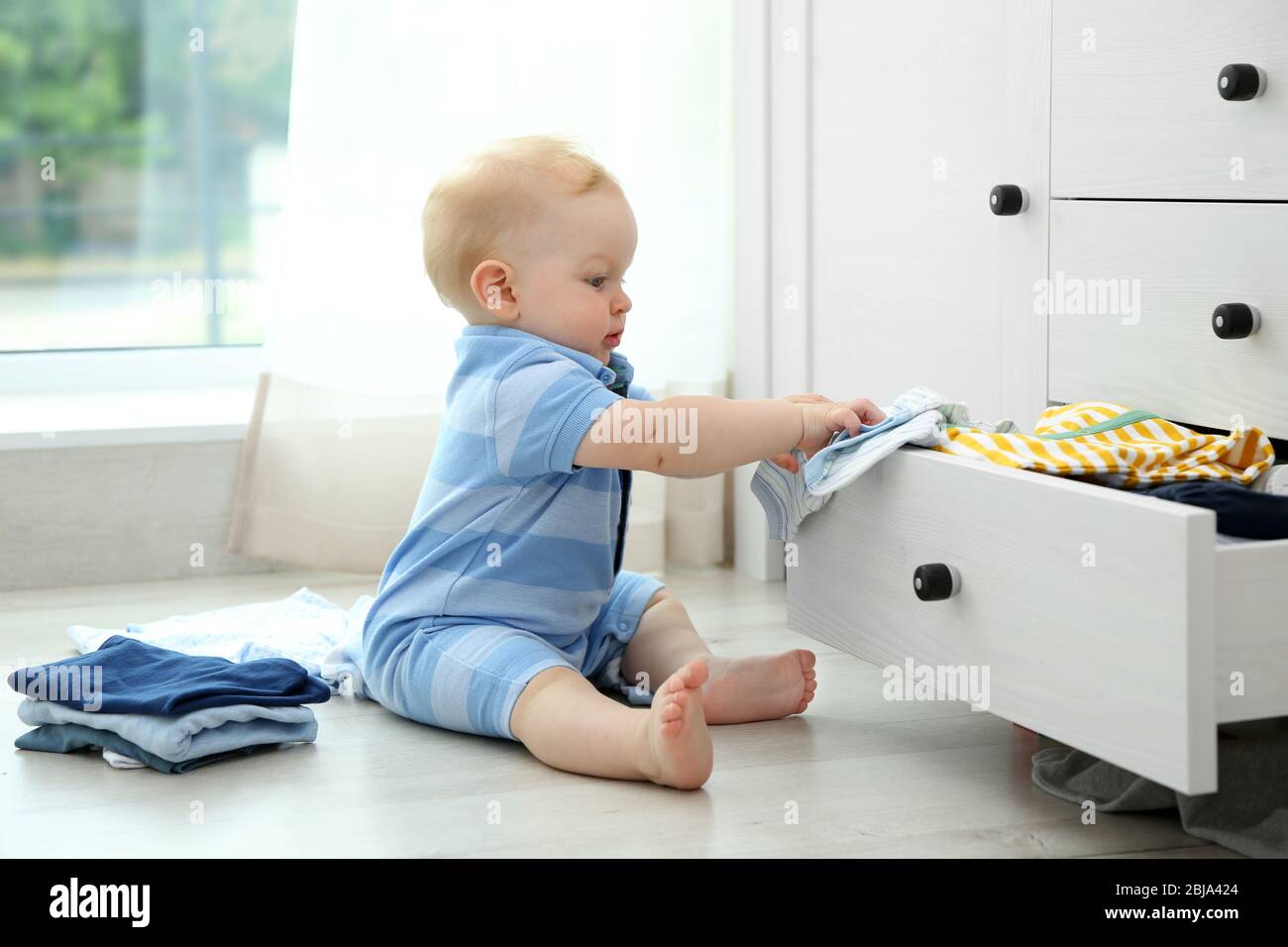 Baby throwing up clothes from wooden chest Stock Photo - Alamy