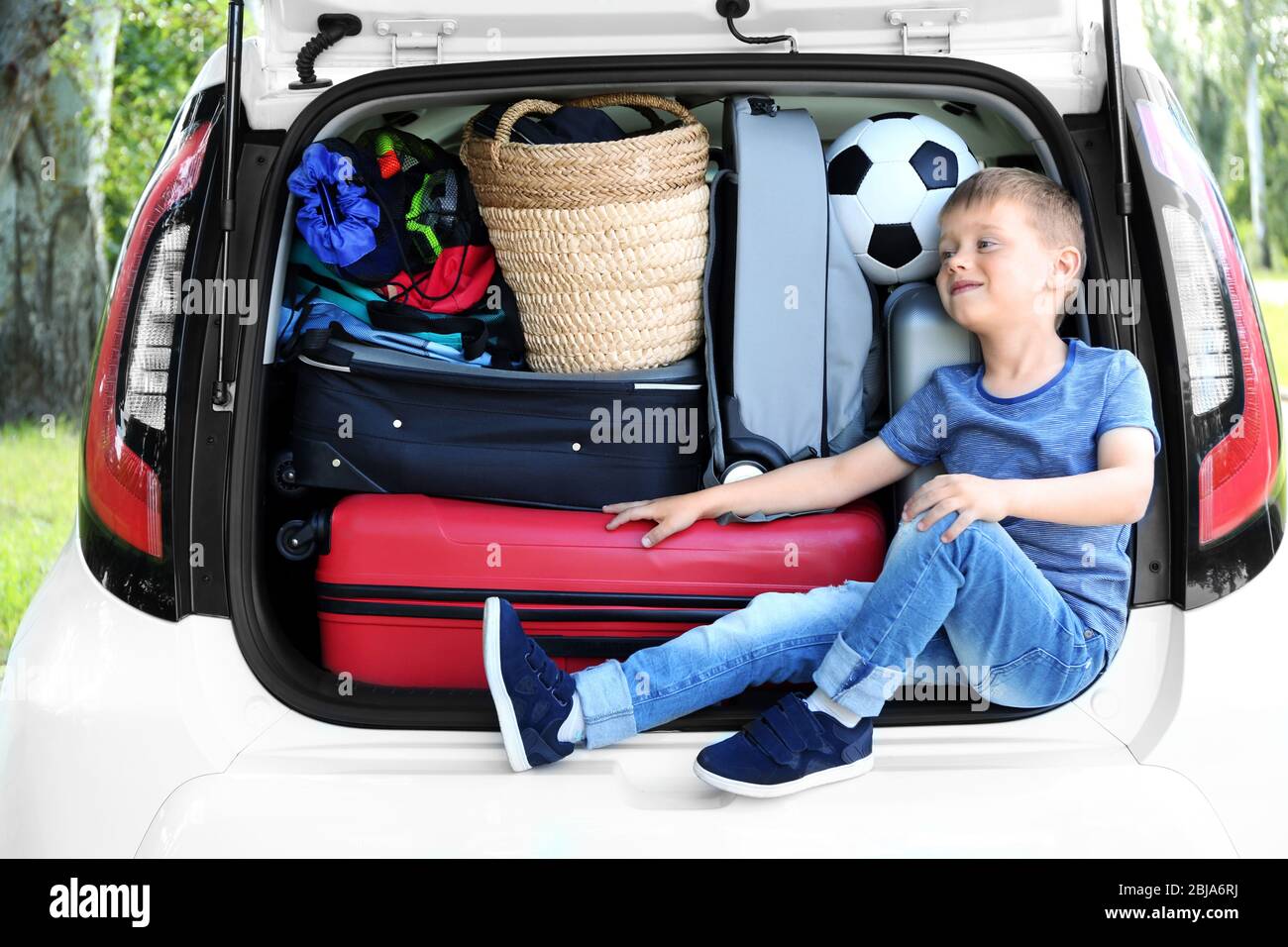 Cute little boy sitting in car trunk full of bags Stock Photo - Alamy