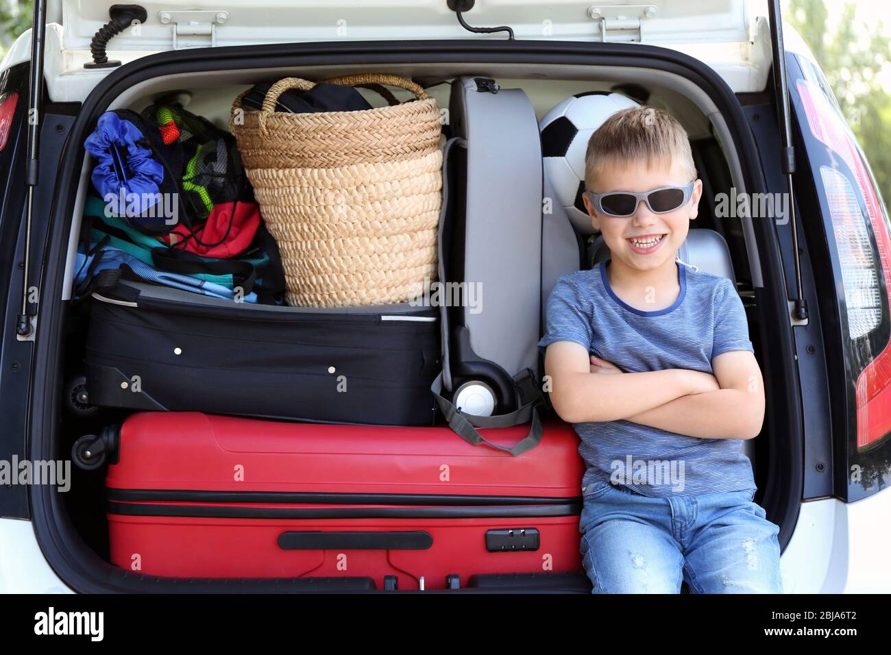 Cute little boy sitting in car trunk full of bags Stock Photo - Alamy