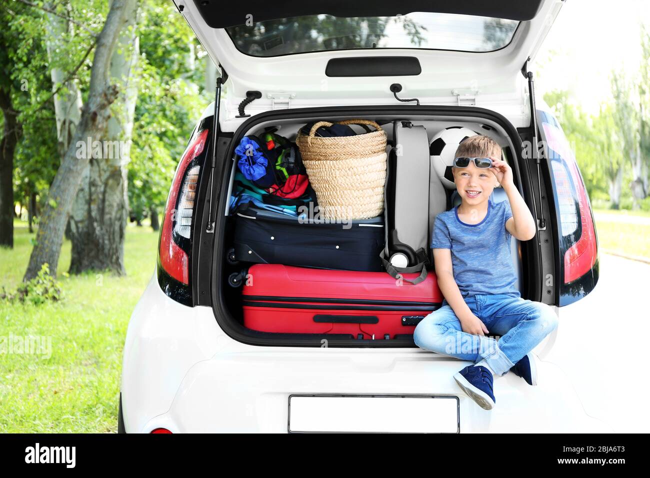 Cute little boy sitting in car trunk full of bags Stock Photo - Alamy