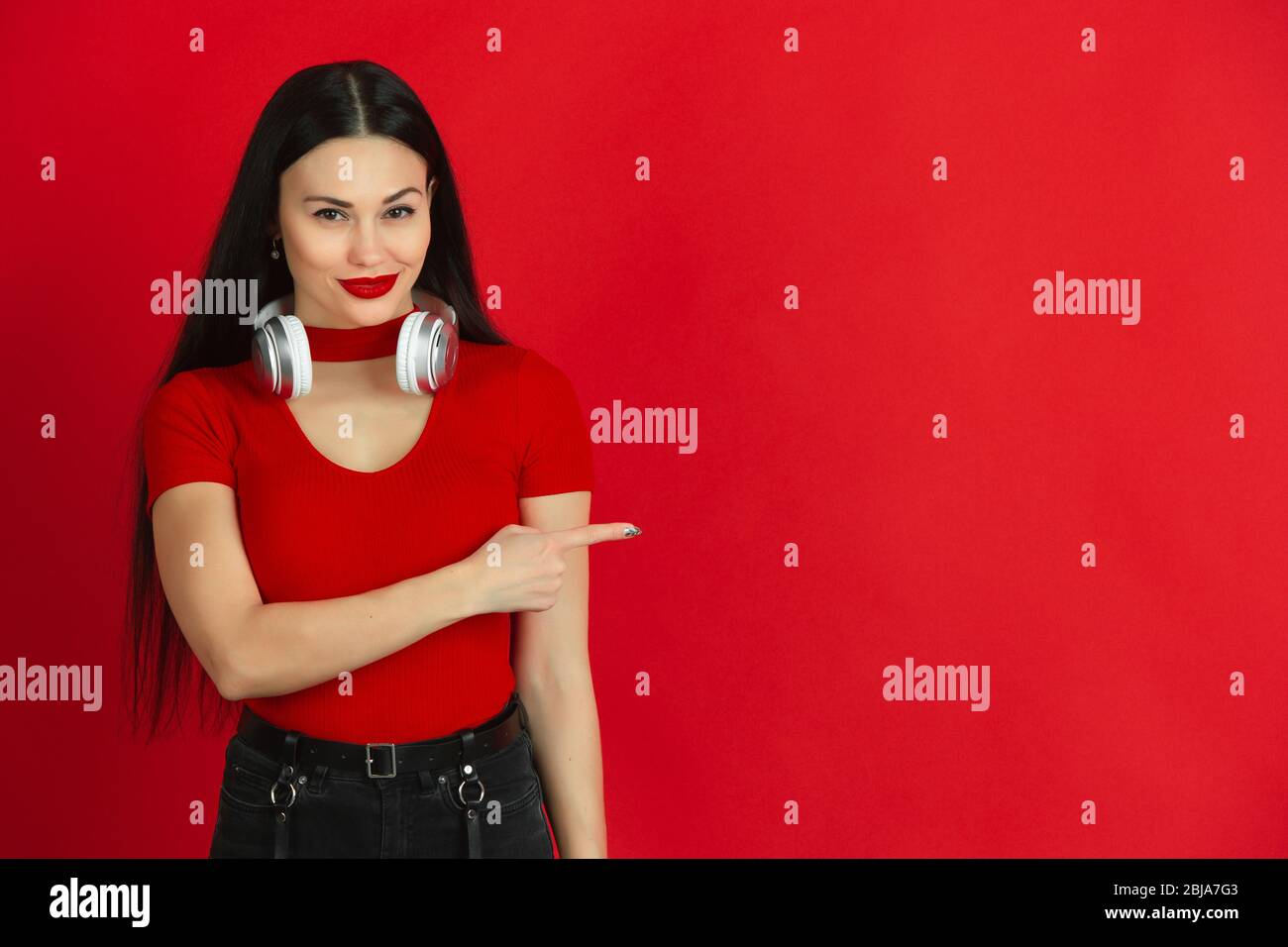 Pointing at side with headphones. Caucasian young woman's monochrome ...