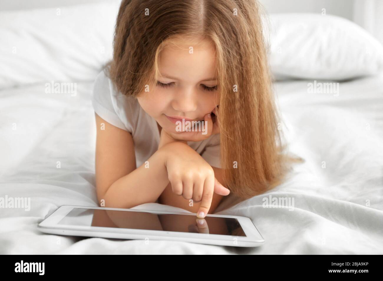 Cute little girl playing with tablet on white bed Stock Photo - Alamy