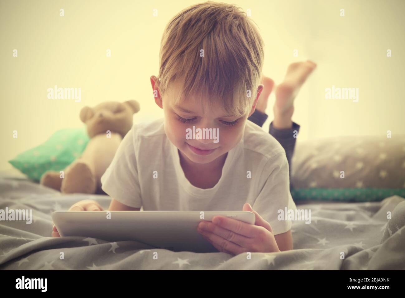 Cute little boy playing with tablet on bed Stock Photo - Alamy