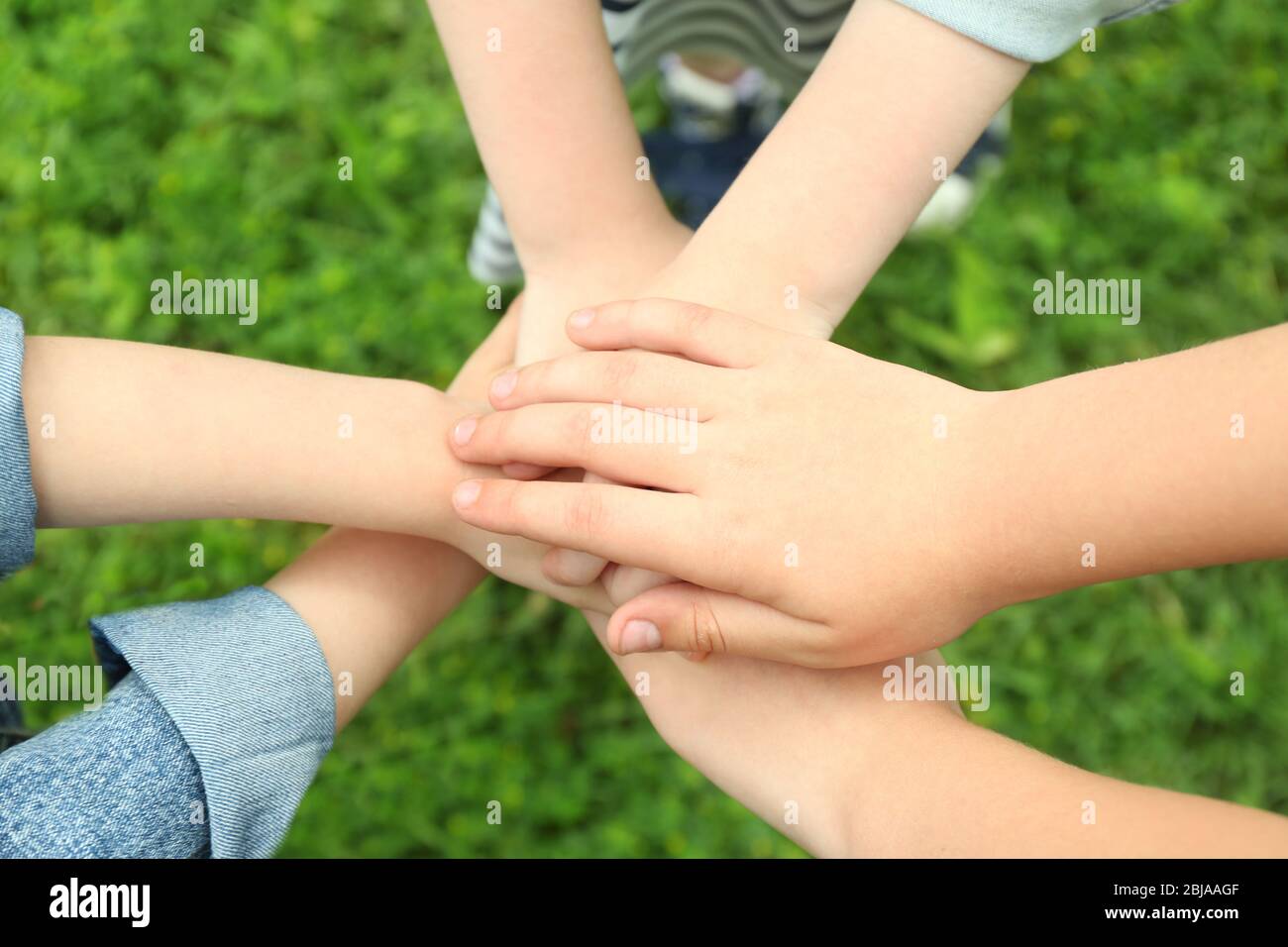 Children holding hands together on grass background Stock Photo - Alamy