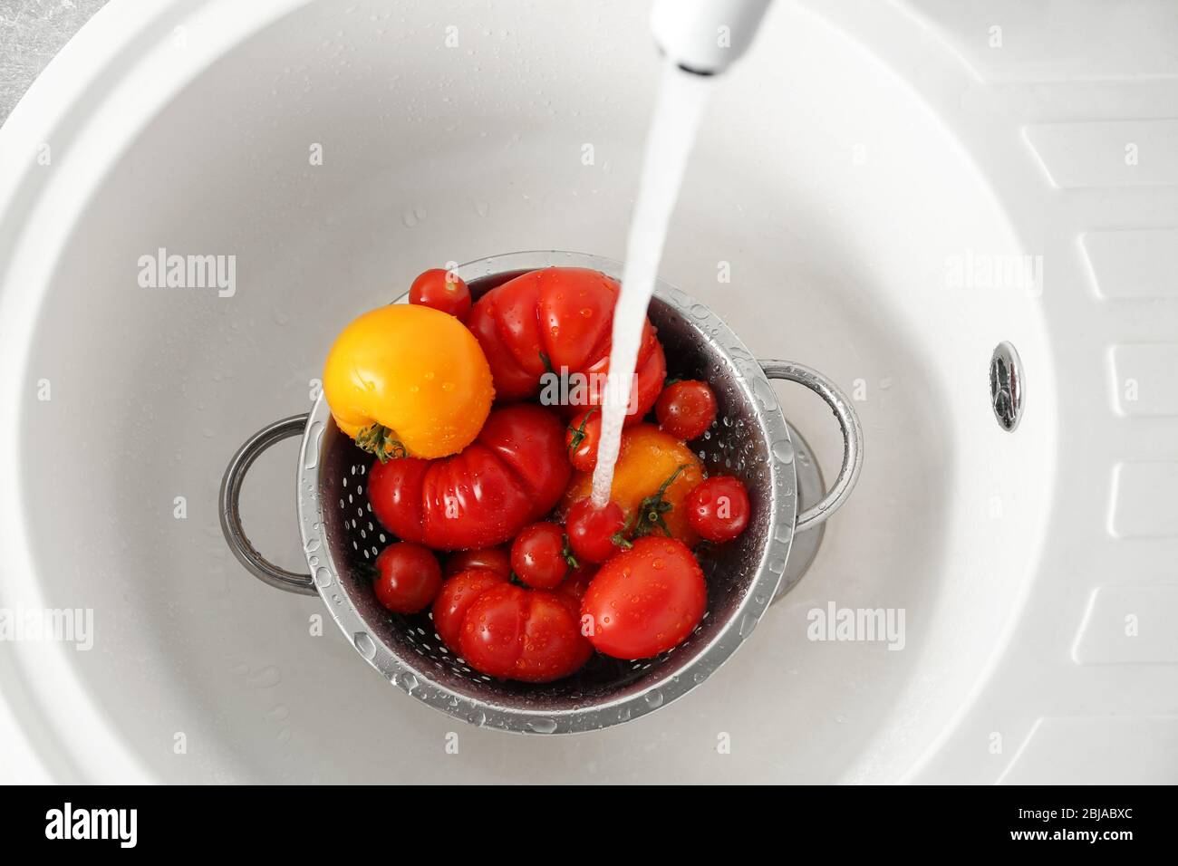 Water flowing into colander with tomatoes in kitchen sink Stock Photo ...