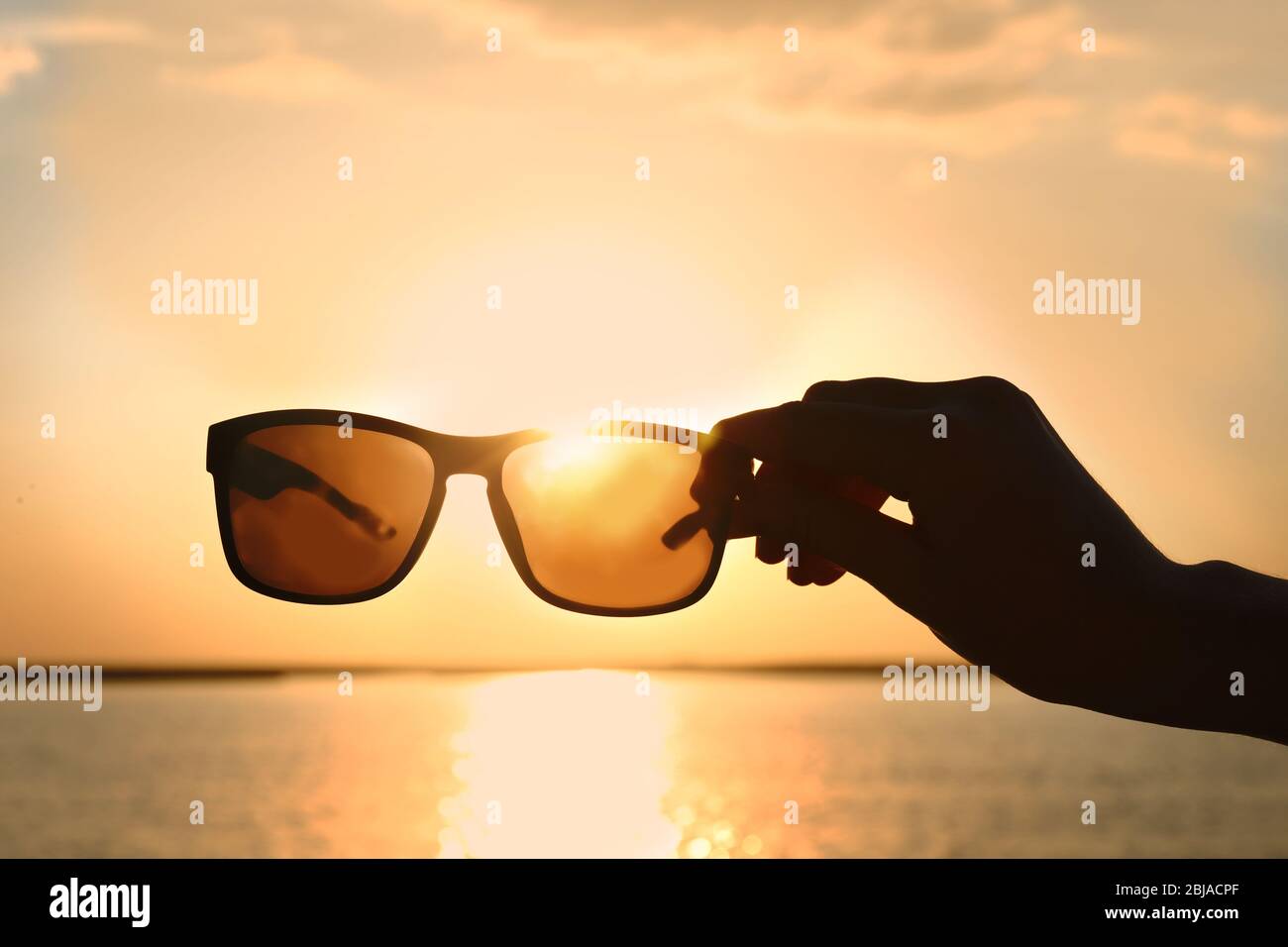 Female hand holding sunglasses on sunset background Stock Photo - Alamy