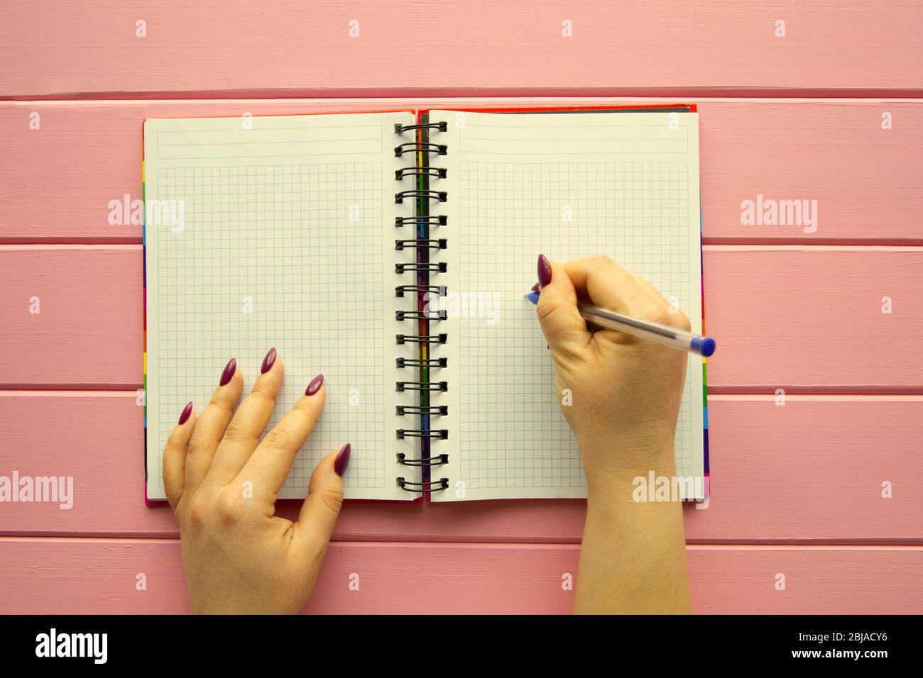 Female hands is writing something in the blank notebook on pink ...