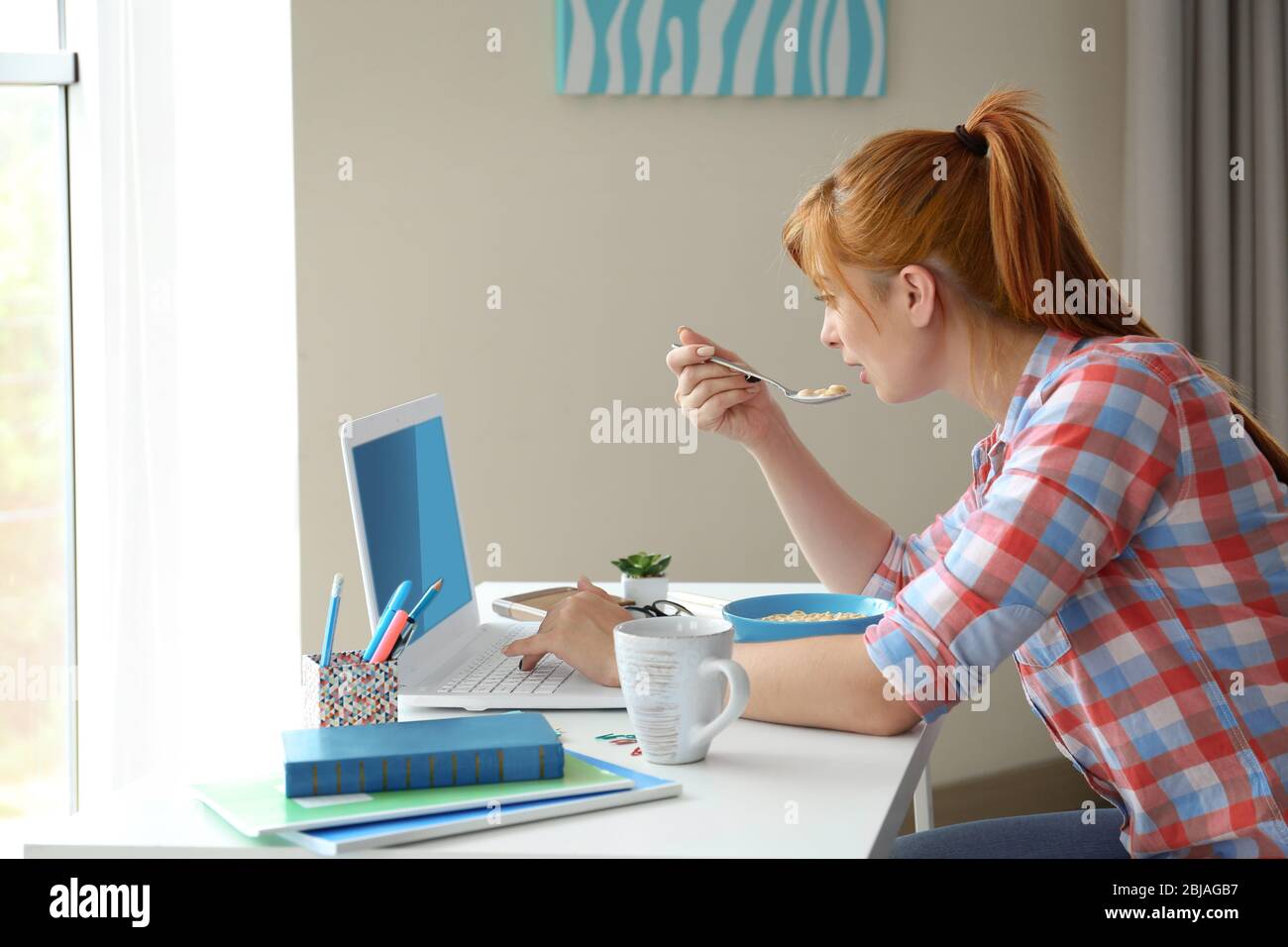 Beautiful girl eating in front of computer Stock Photo - Alamy