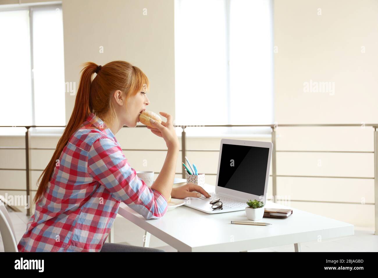 Beautiful girl eating in front of computer Stock Photo - Alamy