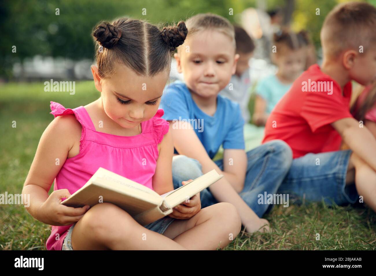 Group of happy kids reading books in park Stock Photo - Alamy
