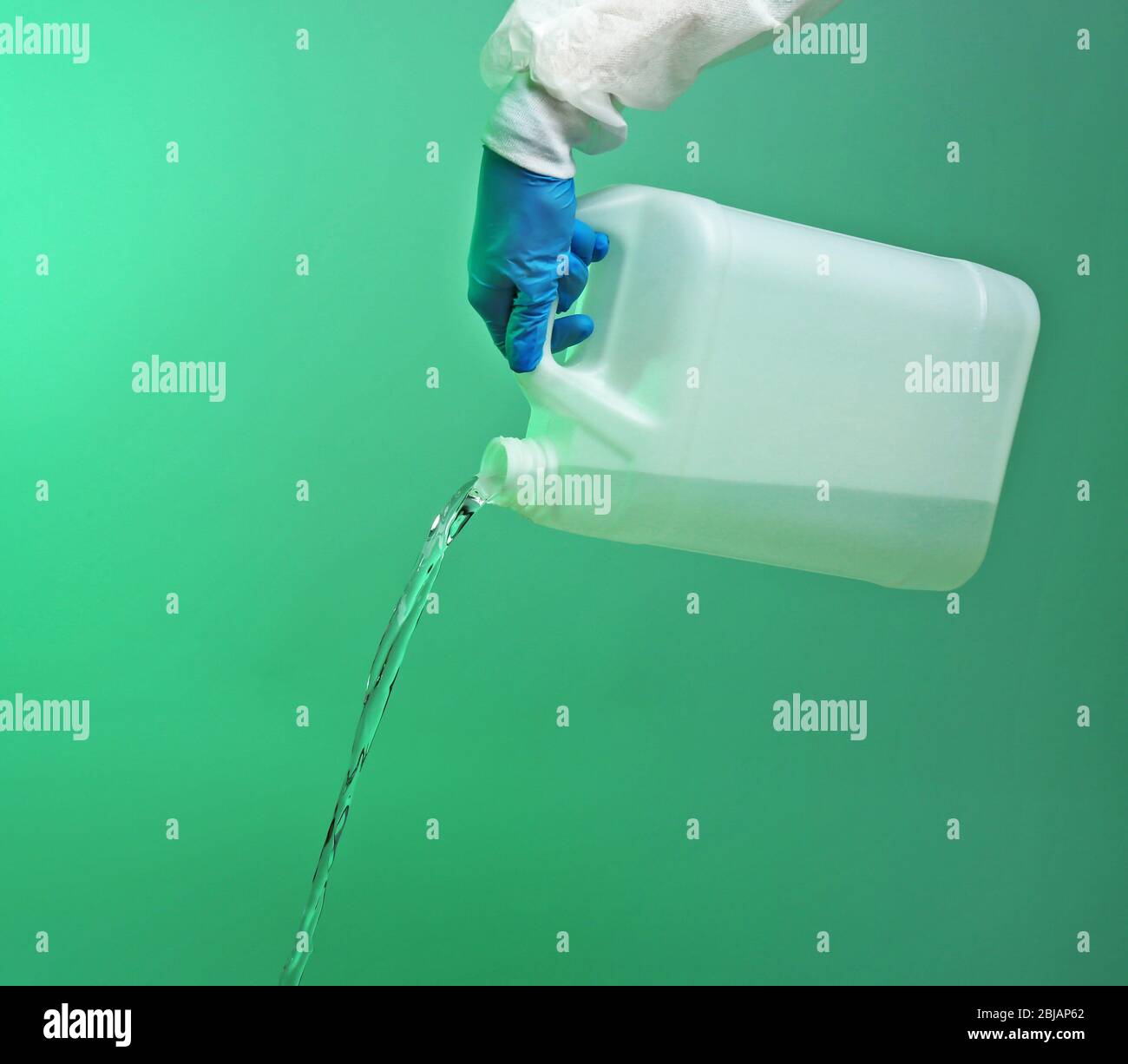Hand in glove pouring water from jerrycan on green background Stock ...