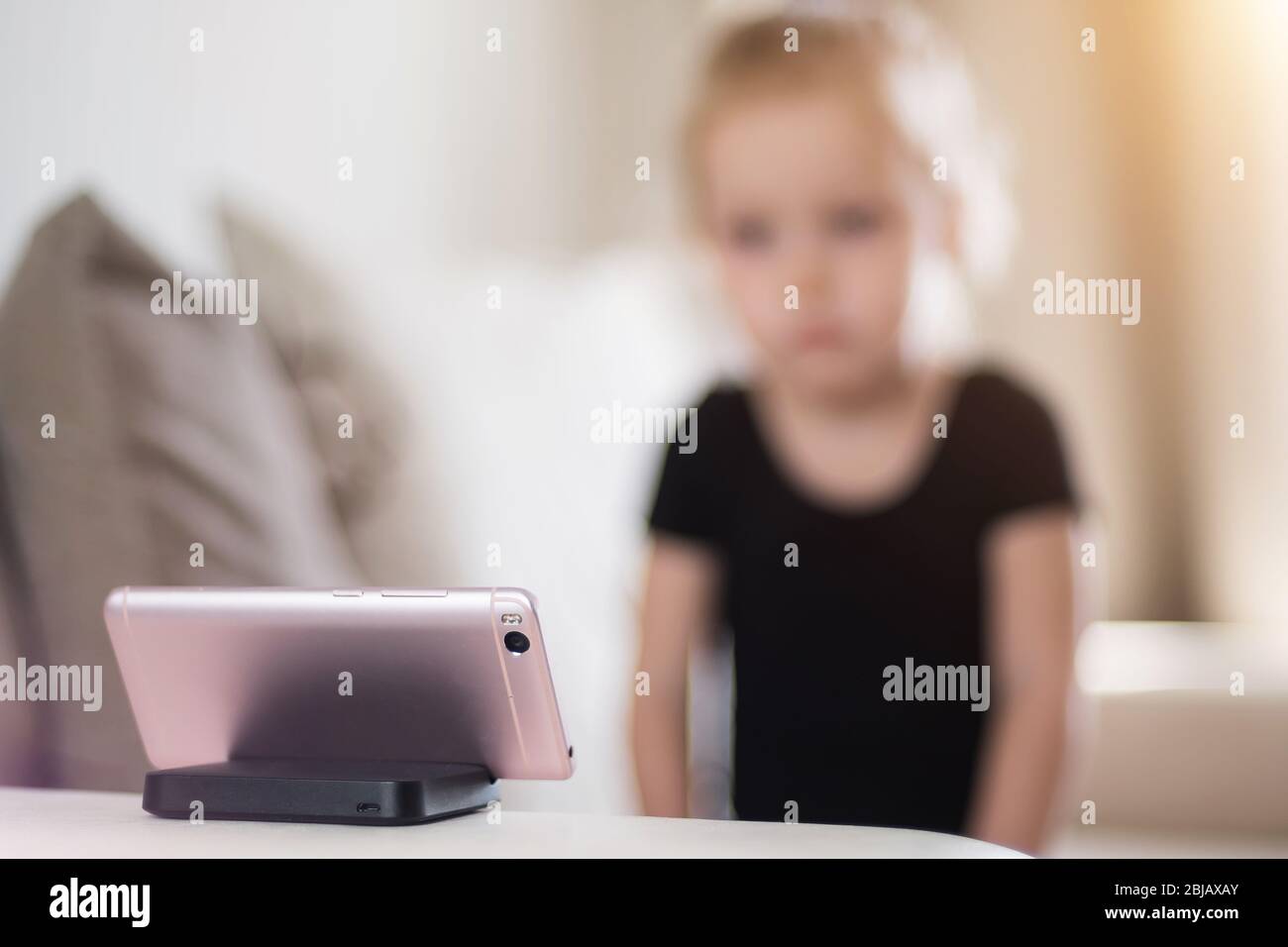 Sad and tired little girl studying at home in front of the smartphone ...