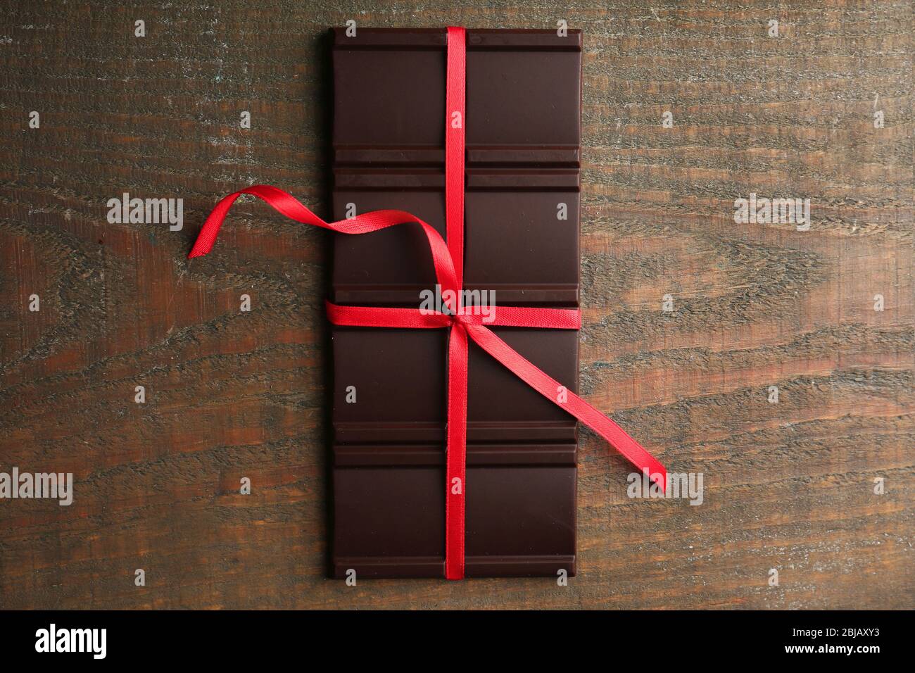 Chocolate bar with red ribbon on wooden background Stock Photo - Alamy