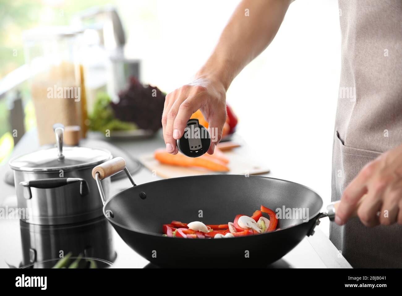 Male hand adding salt to vegetables in pan closeup Stock Photo - Alamy