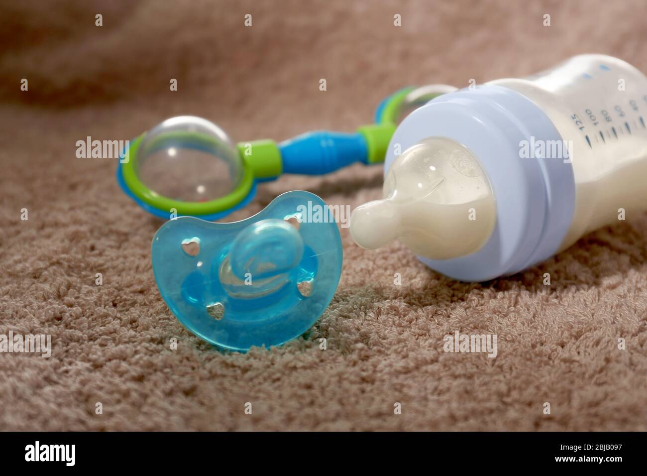 Feeding bottle with baby milk formula, pacifier and rattle toy on towel ...