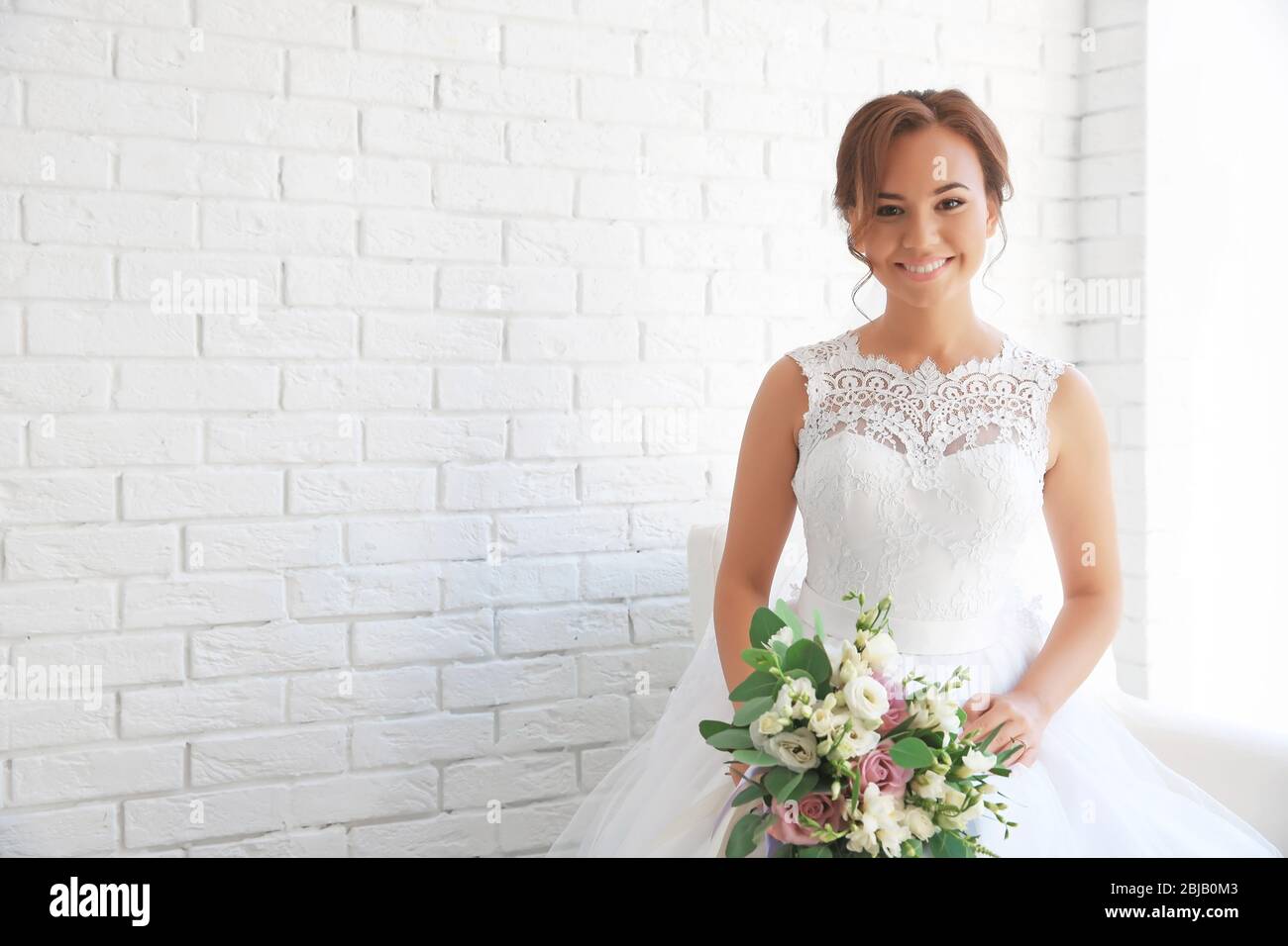 Beautiful bride with wedding bouquet on white brick wall background ...