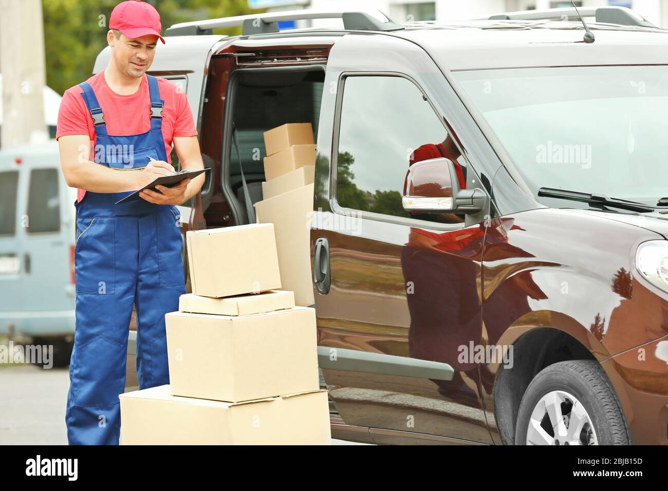 Delivery concept. Postman with parcels near a car Stock Photo - Alamy