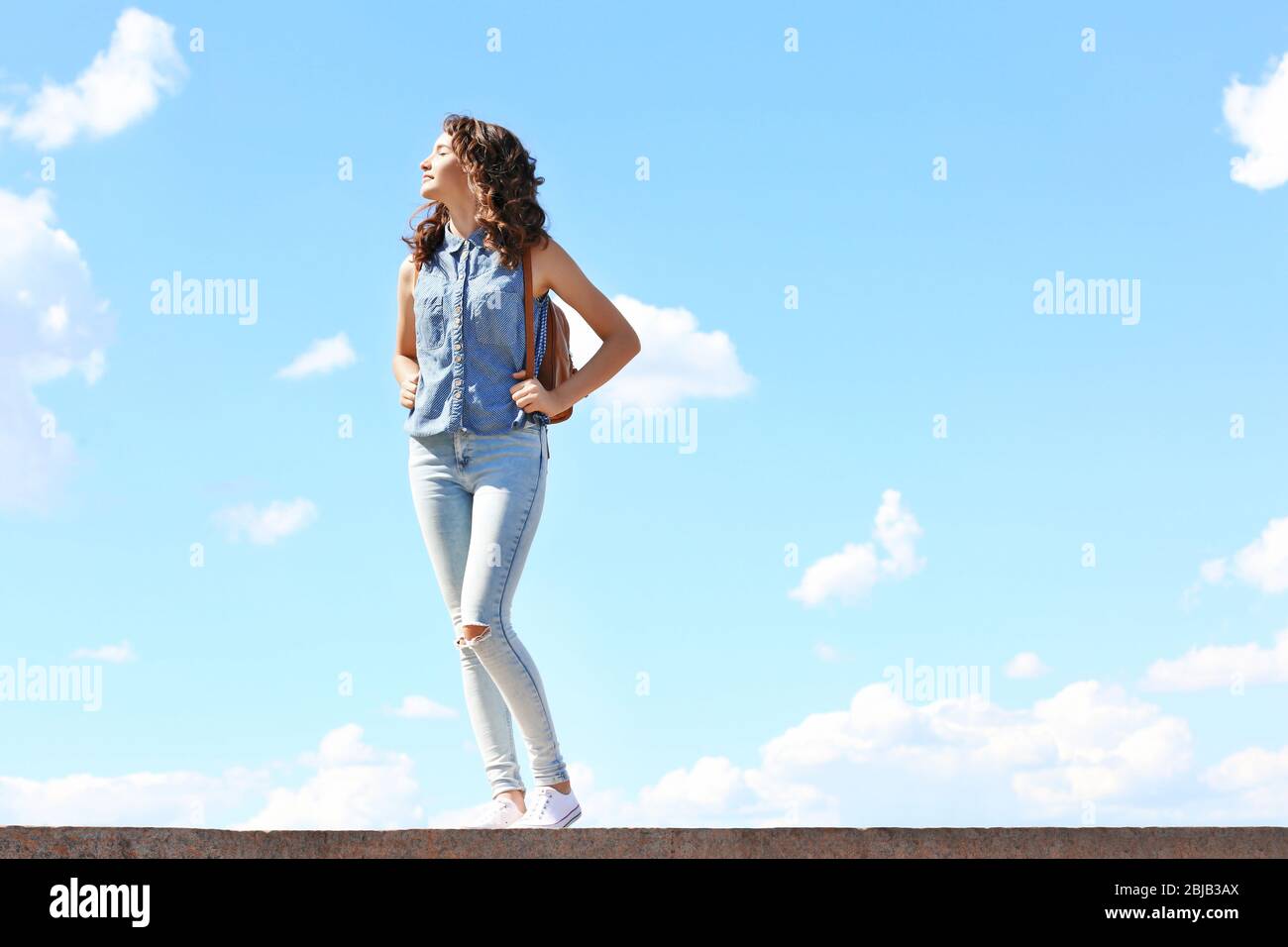 Beautiful young girl posing on blue sky background Stock Photo - Alamy
