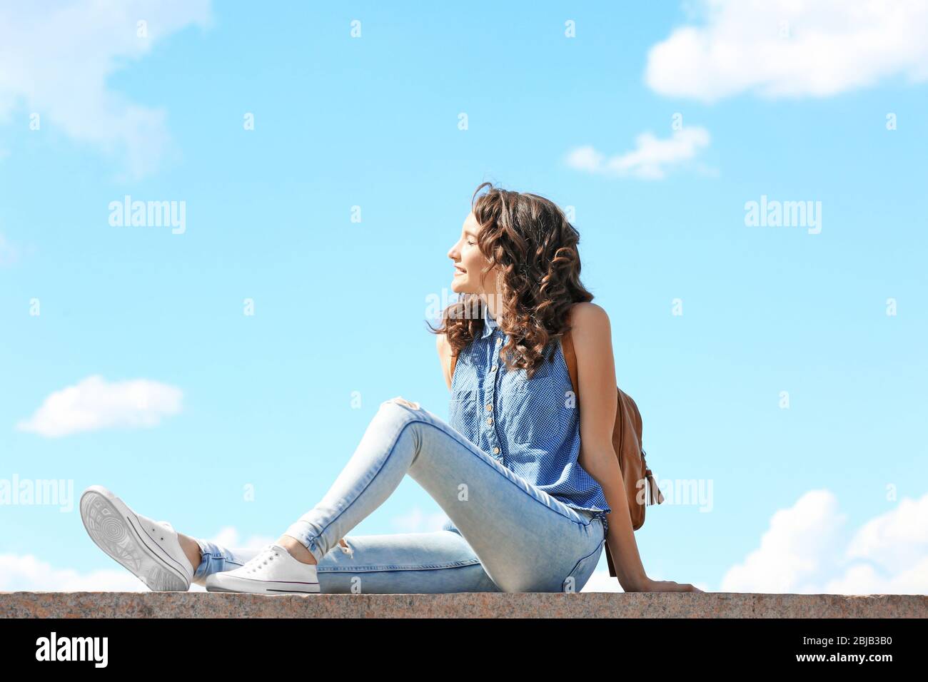 Beautiful young girl posing on blue sky background Stock Photo - Alamy
