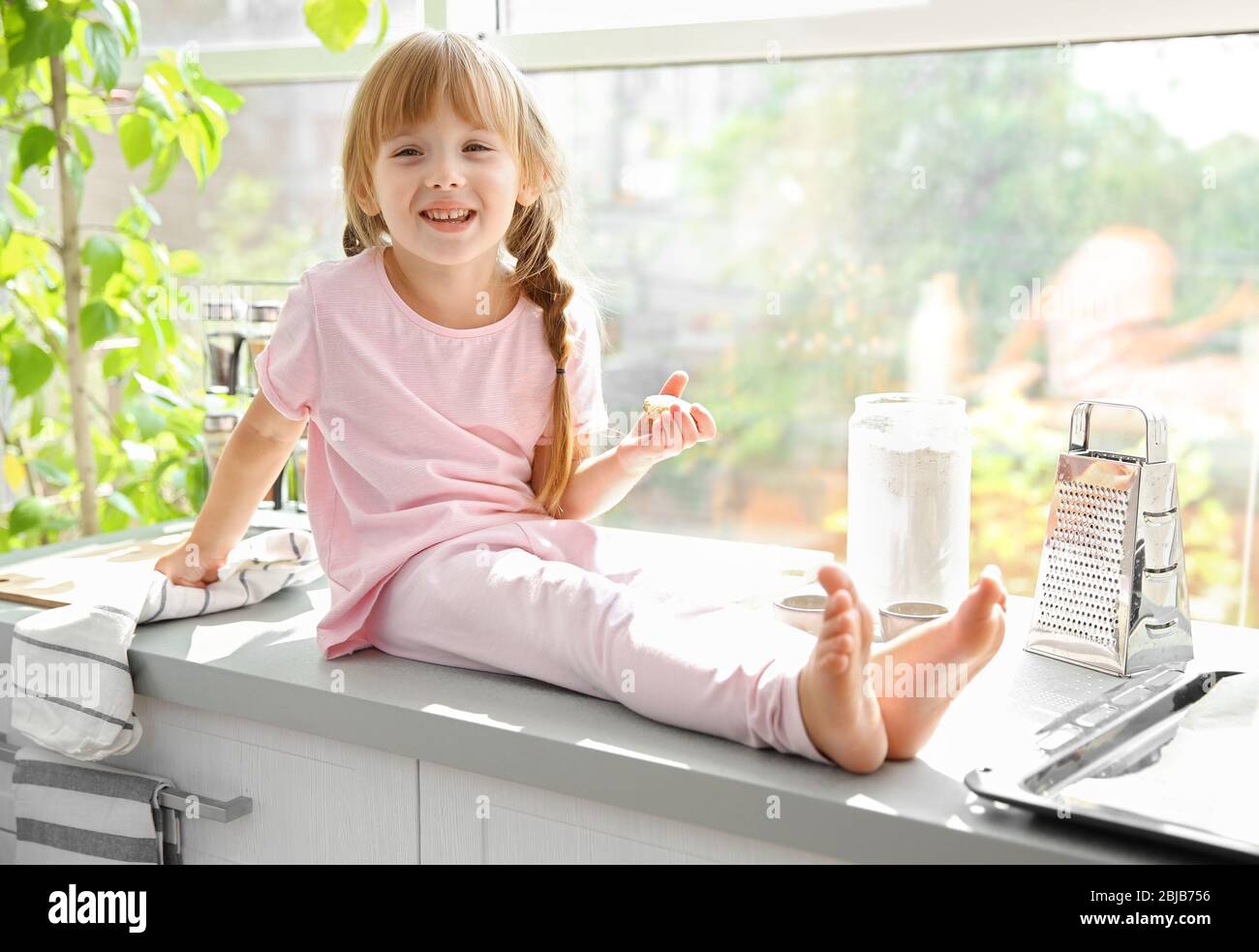 Cute little girl sitting on table in kitchen Stock Photo - Alamy