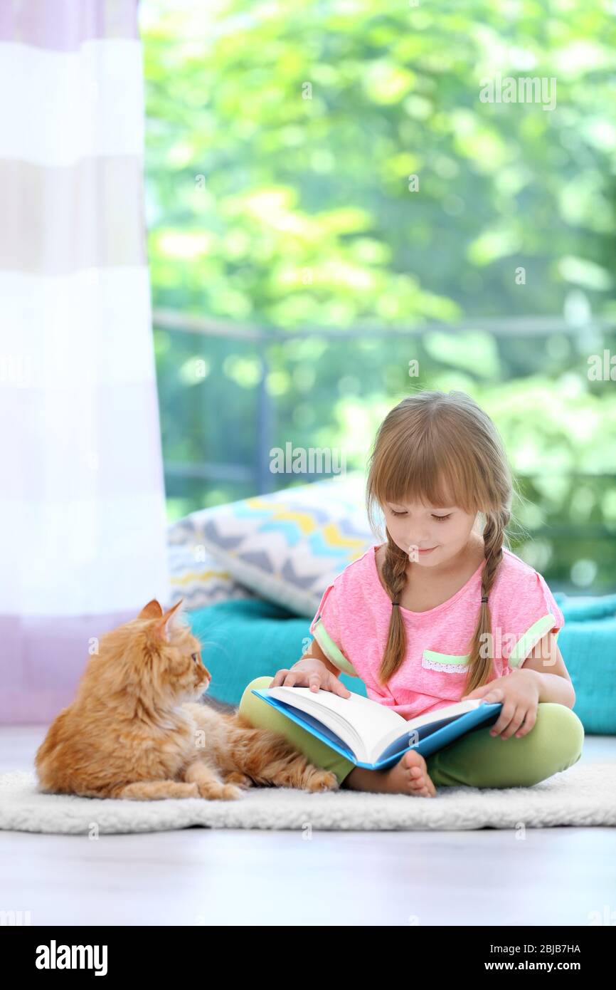 Red cat and cute little girl reading book on carpet Stock Photo - Alamy