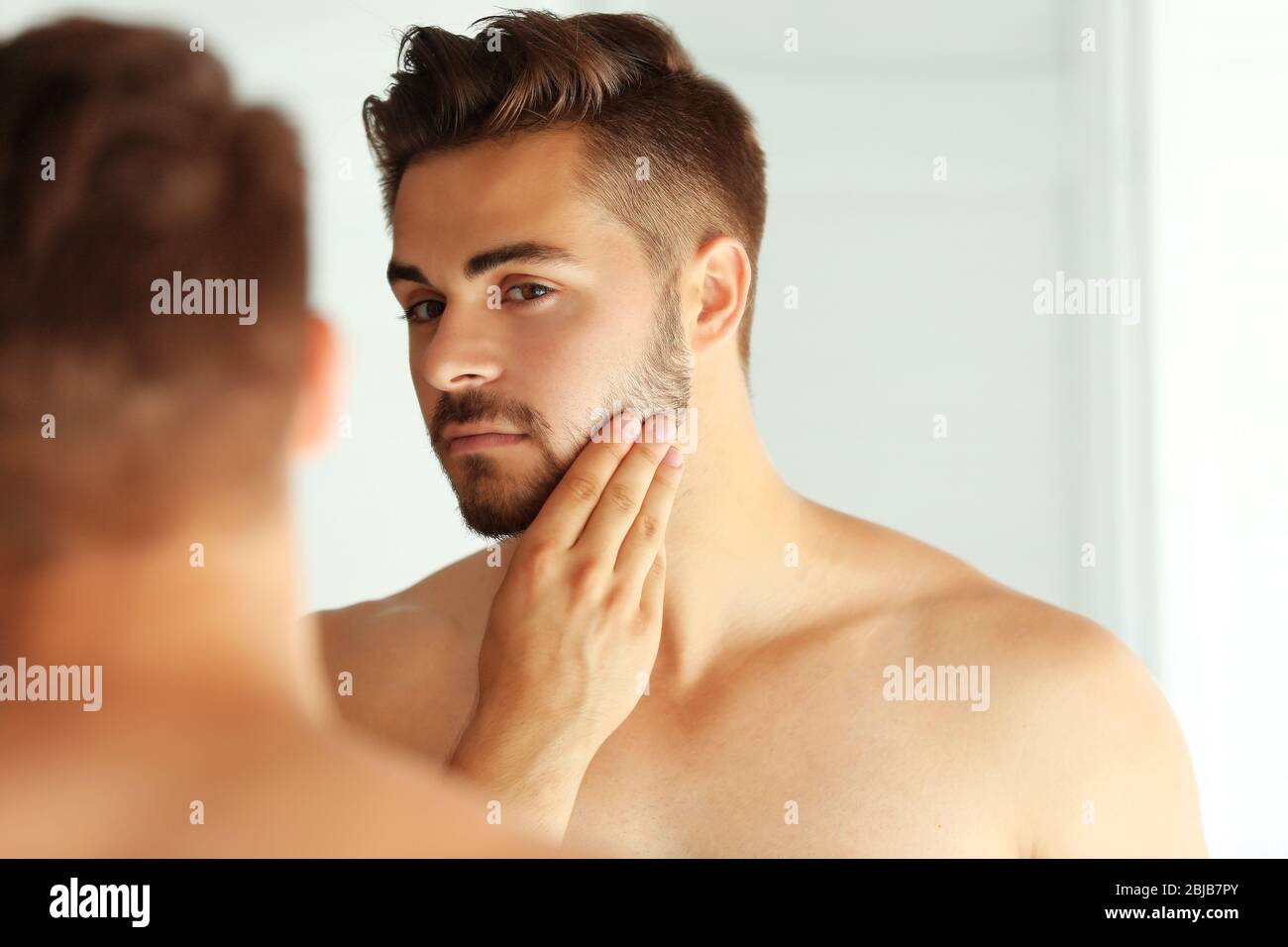 Handsome unshaven man looking in mirror Stock Photo - Alamy