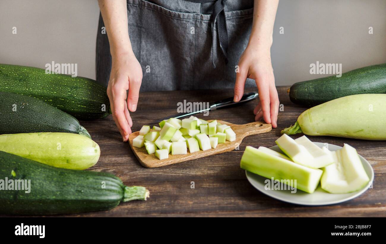 Zucchini harvest. Woman slices zucchini cubes for freezing on wooden ...