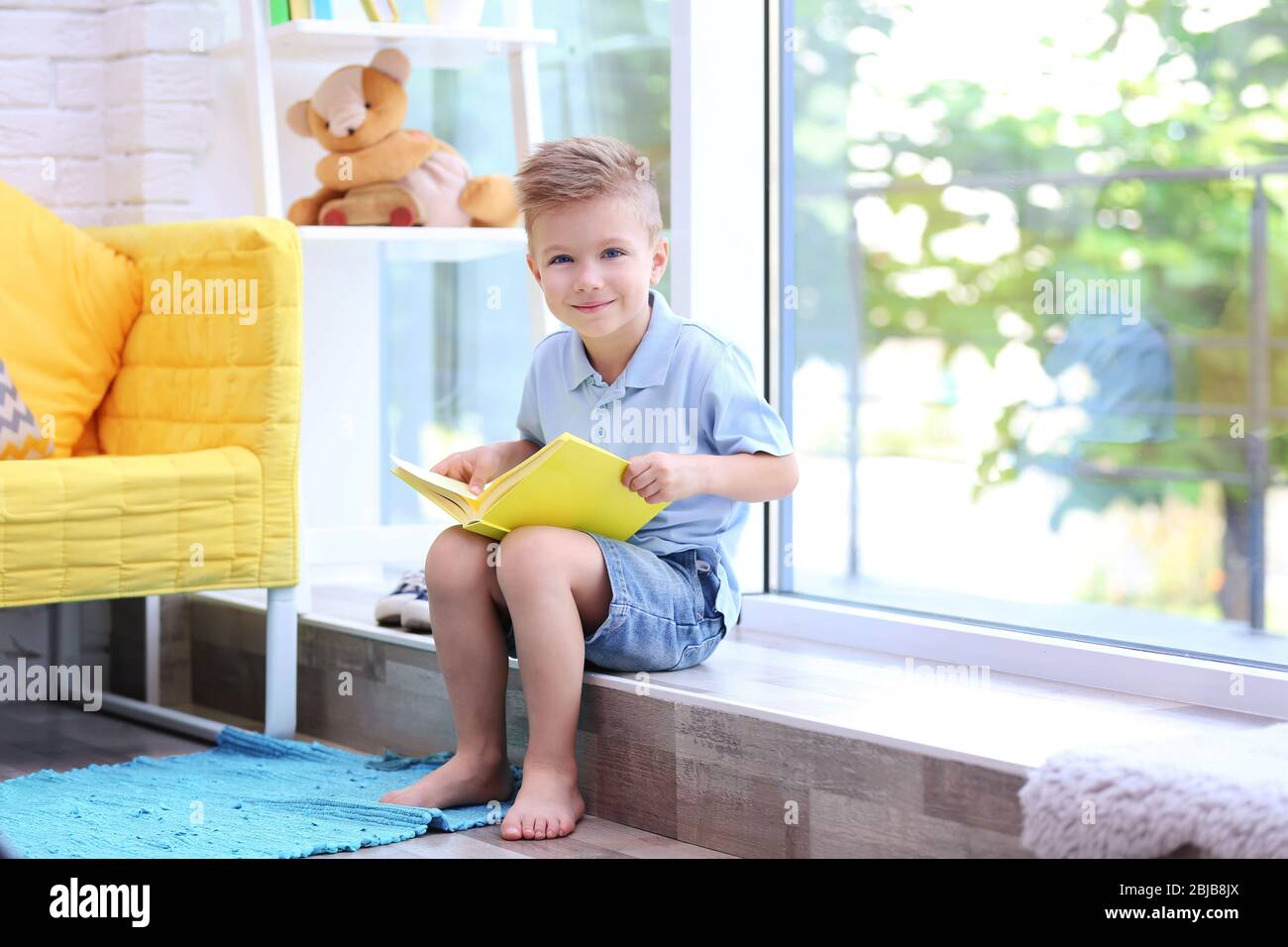 Cute boy reading interesting book on windowsill Stock Photo - Alamy