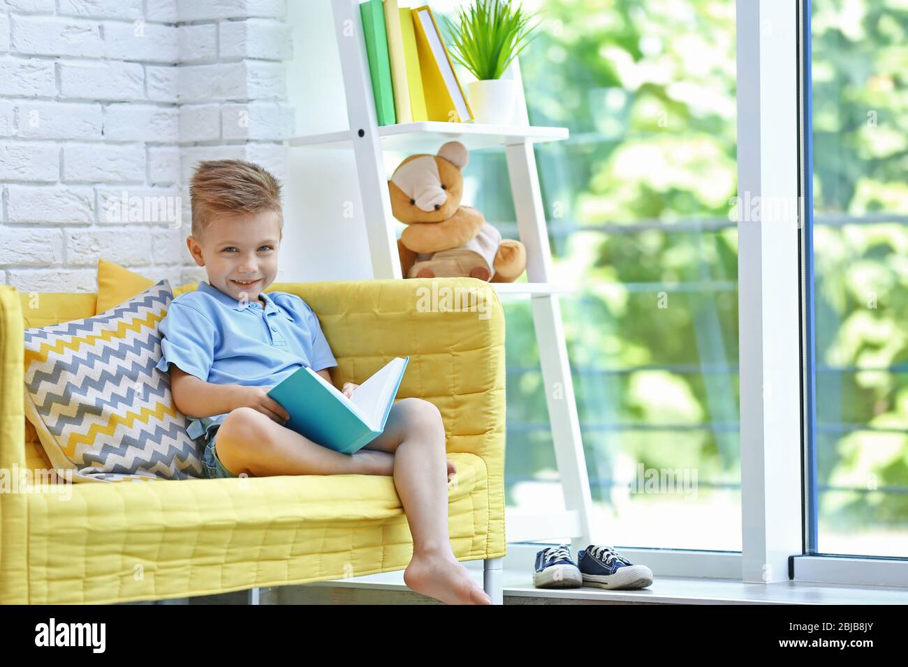 Little boy sitting on sofa and reading book Stock Photo - Alamy