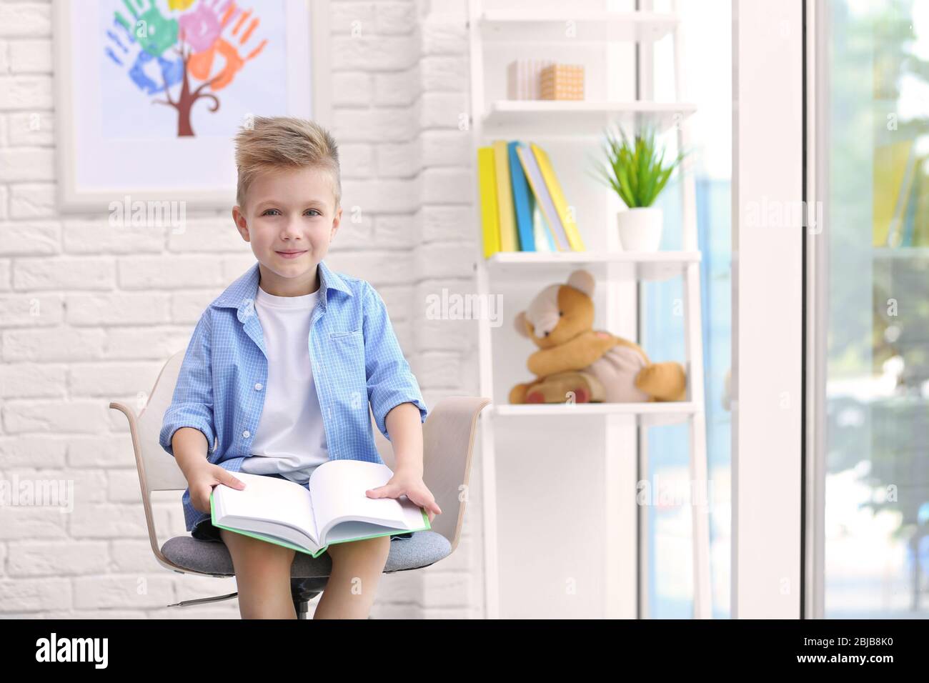 Cute boy sitting on chair and reading book Stock Photo - Alamy