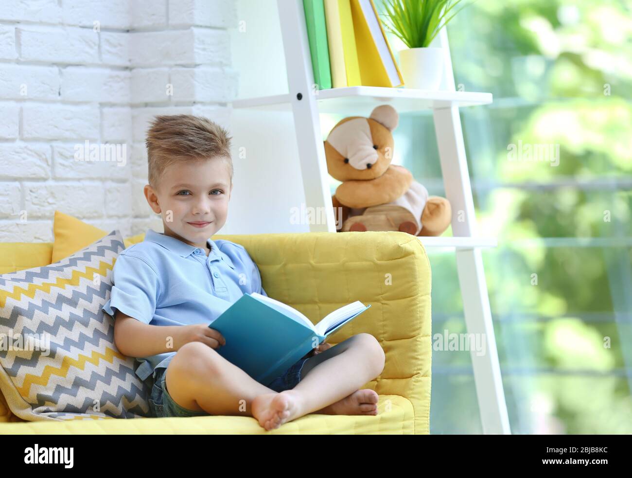 Little boy sitting on sofa and reading book Stock Photo - Alamy